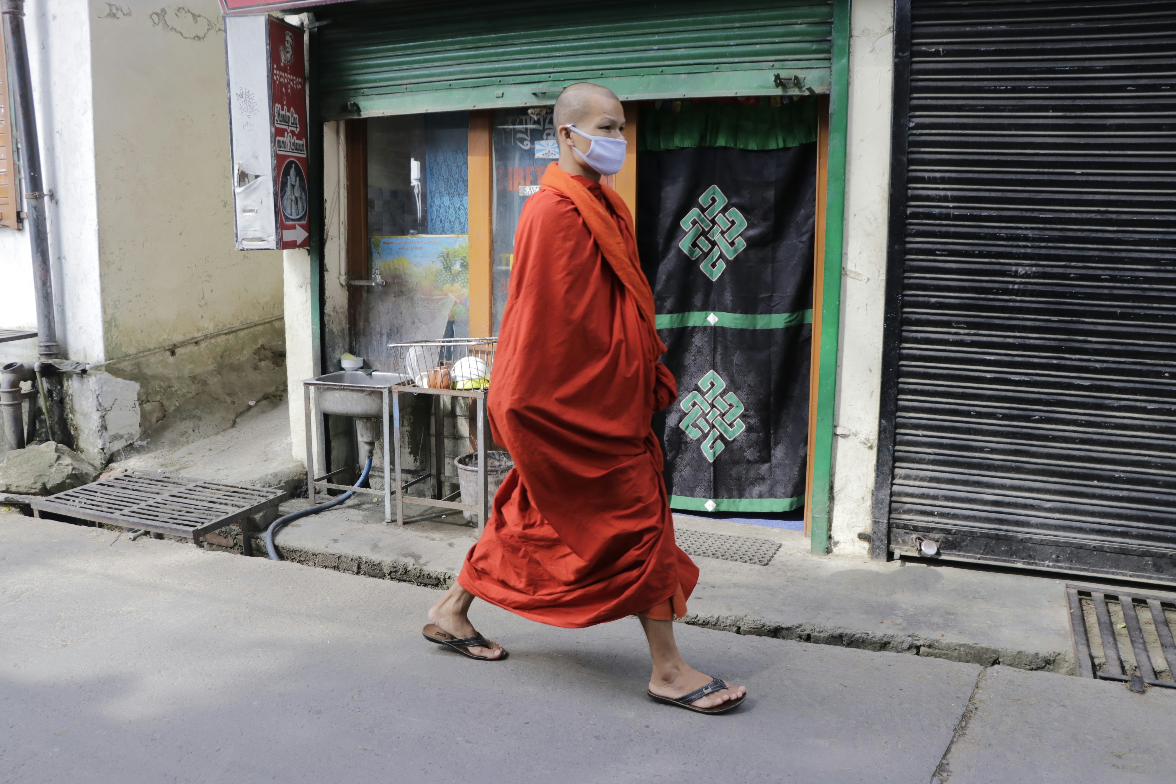Orange-Robed Monk Strides Past a Shuttered Shopfront