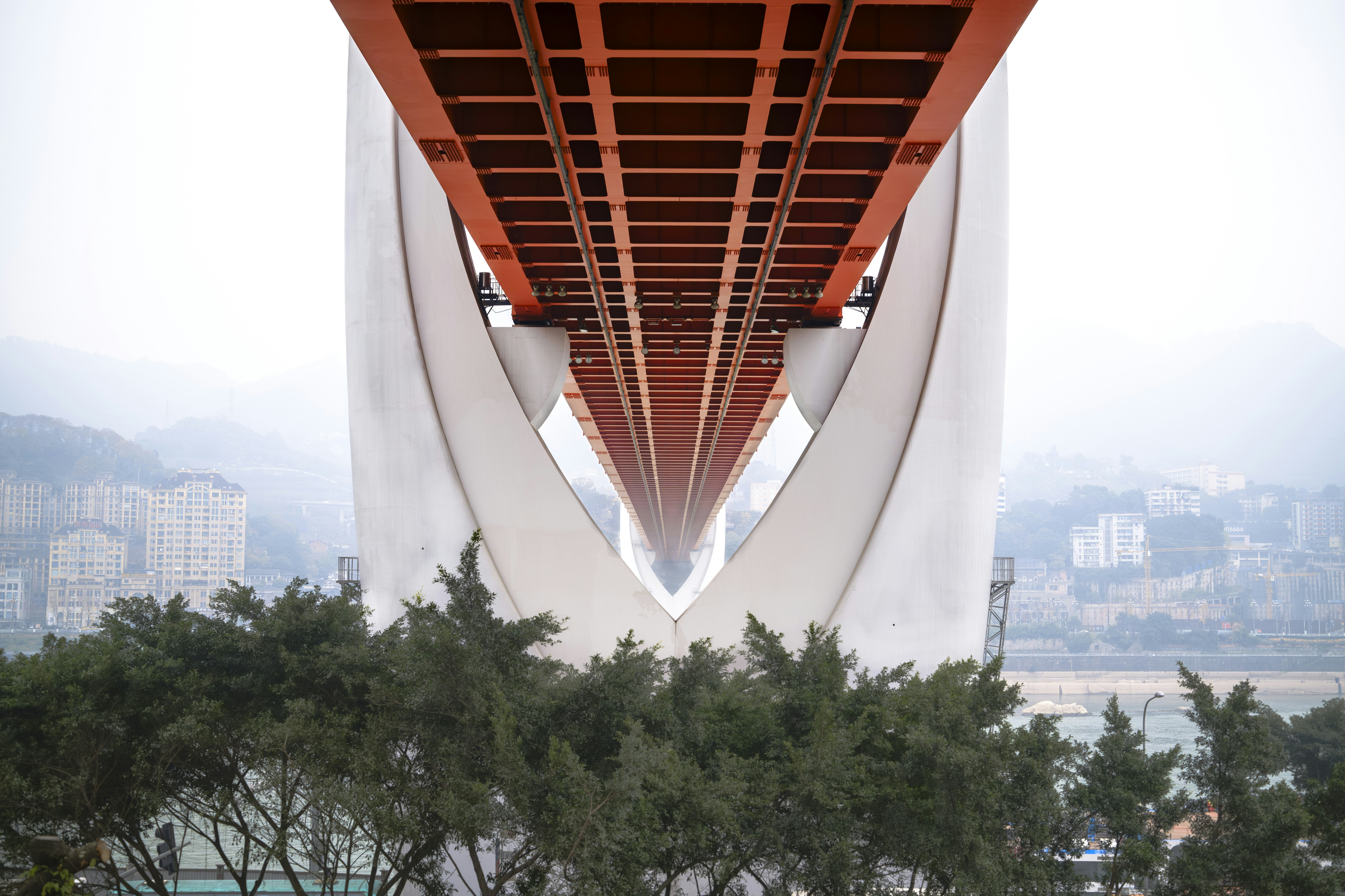 View from beneath a bridge with urban skyline and lush trees in the misty background.