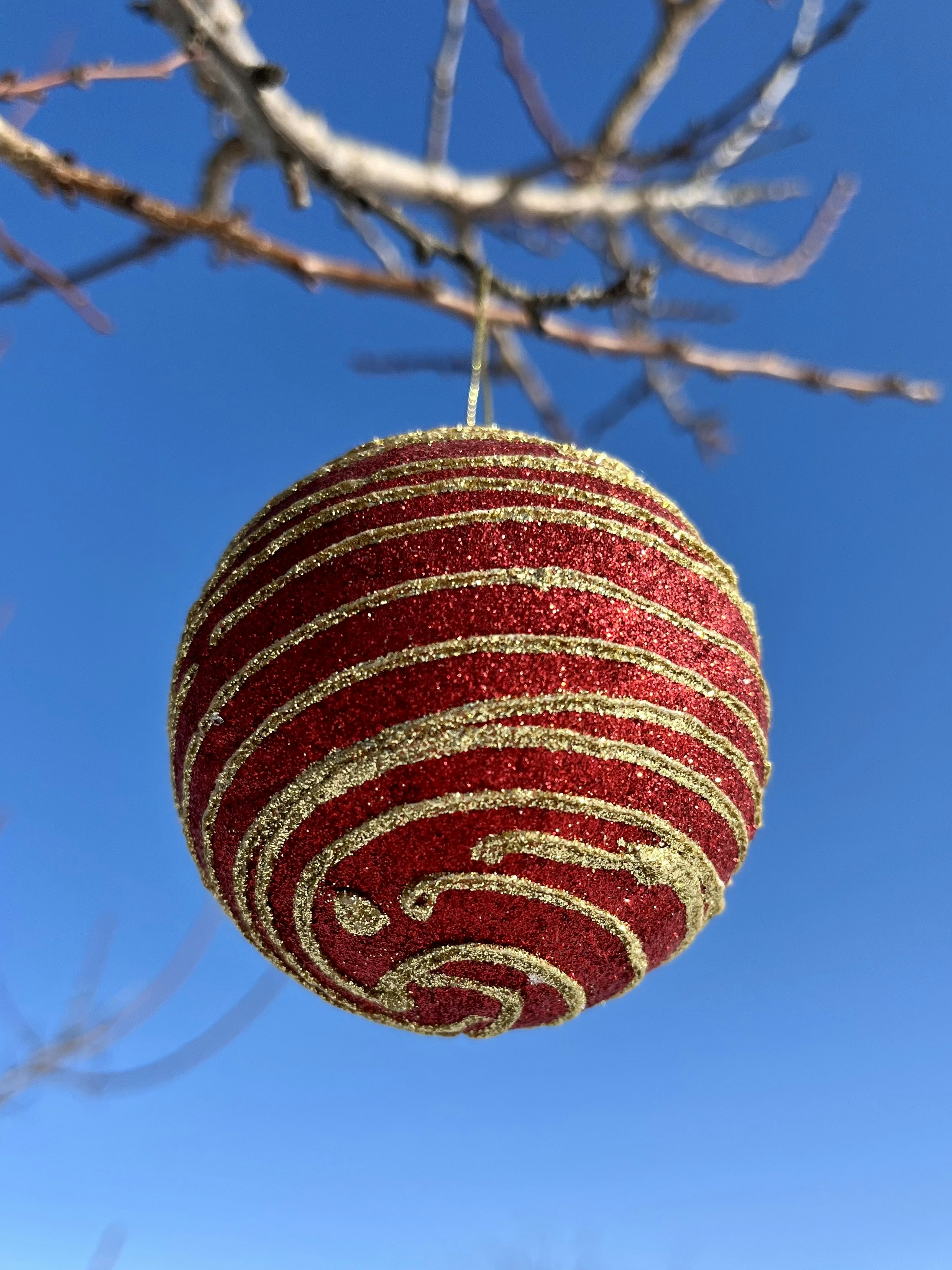 Red Glitter Orb with Gold Spiral Rings Against a Clear Winter Sky