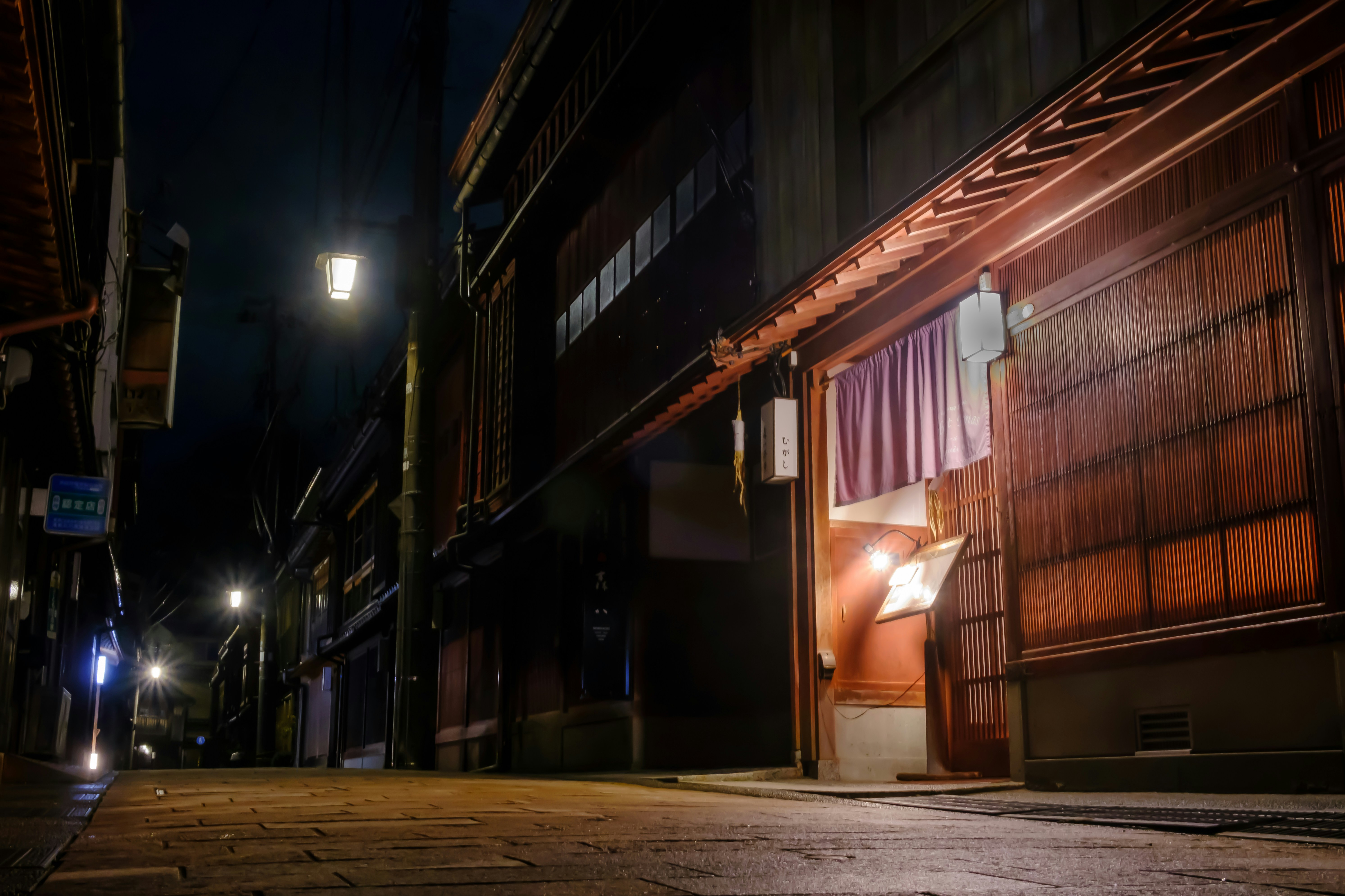 Dimly lit traditional street with wooden buildings and glowing lanterns at night.