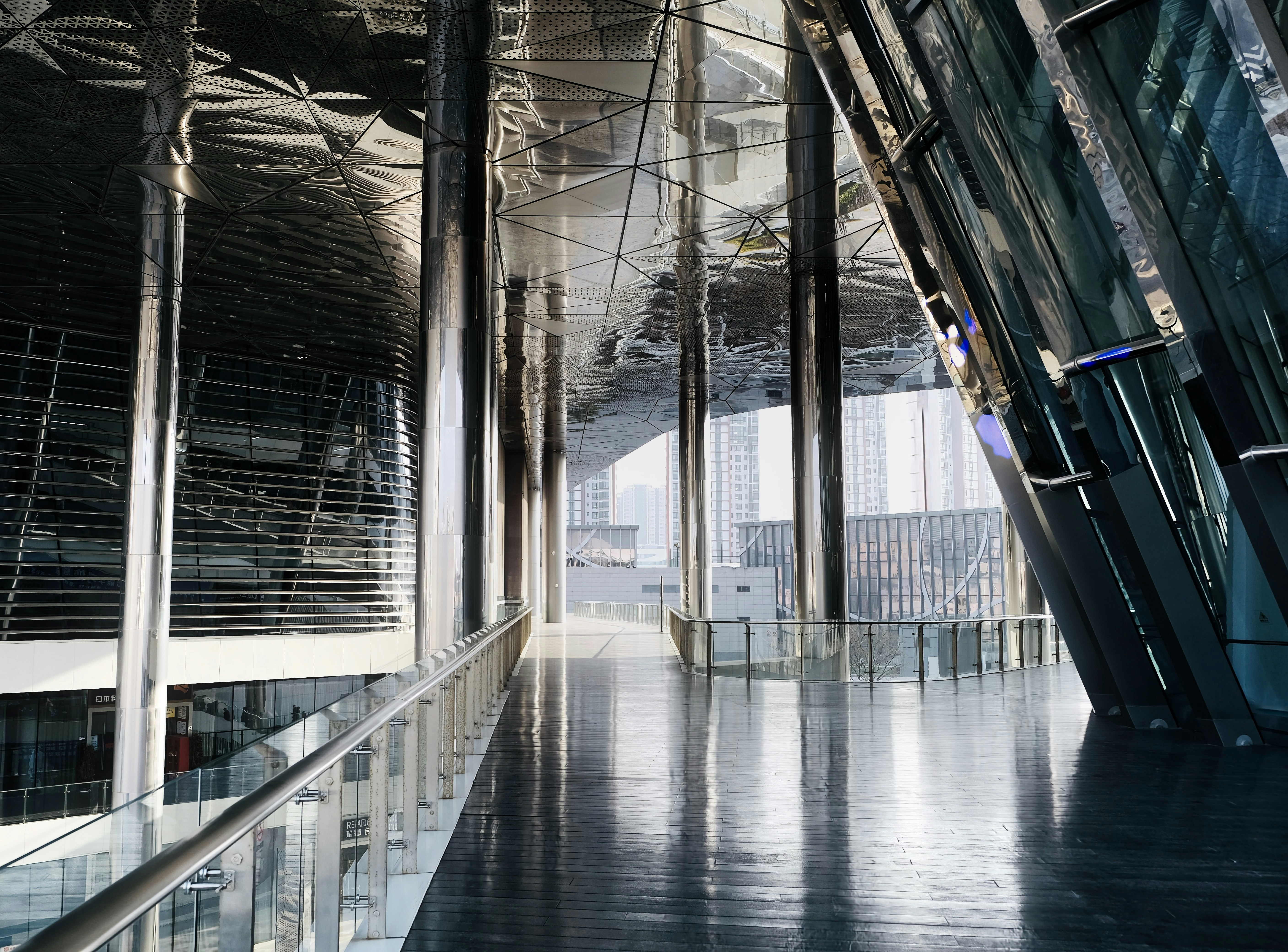 Modern architectural corridor with reflective glass and polished floors, featuring towering metallic columns.