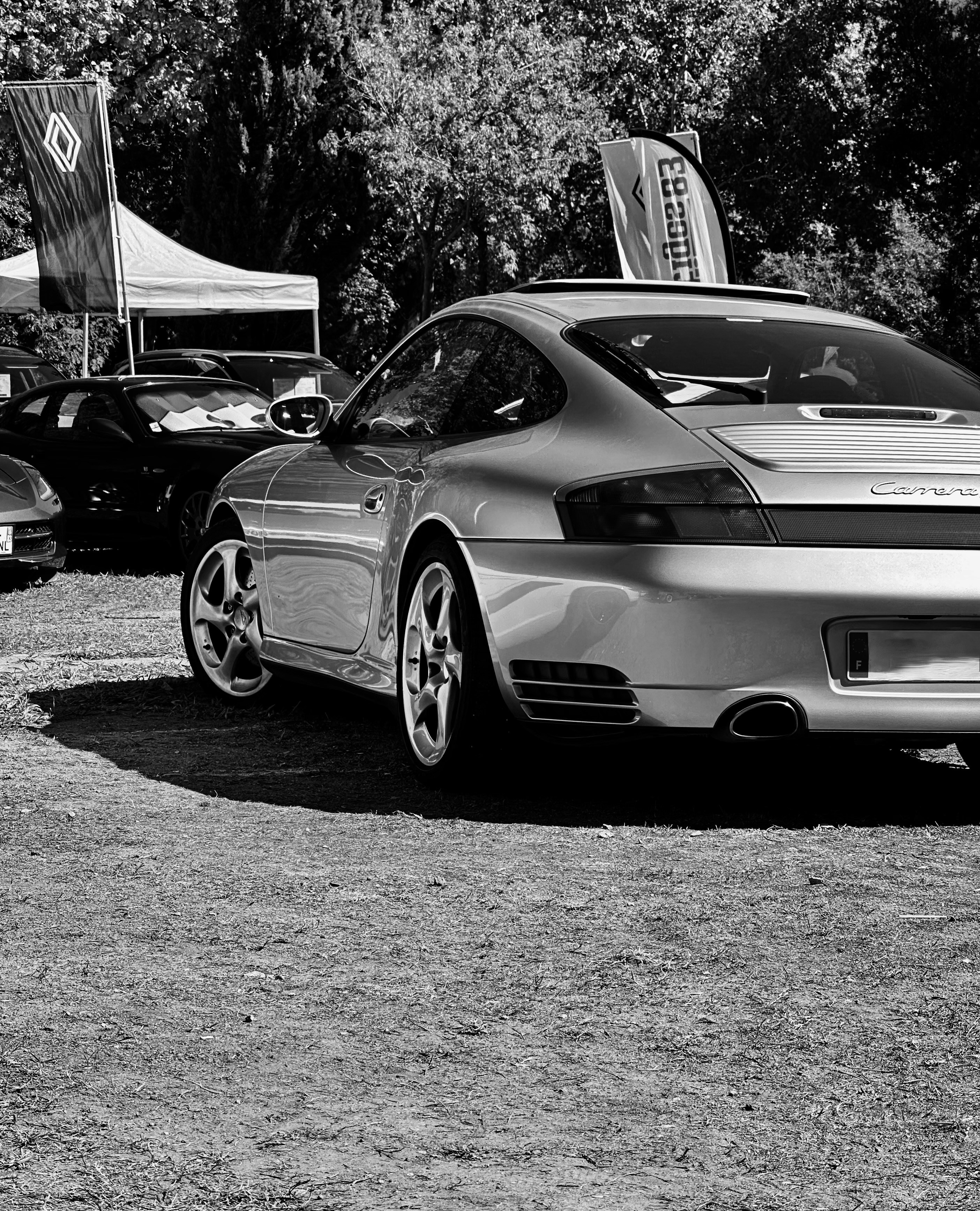 Silver Porsche 911 parked on grass, showcasing its sleek design against a backdrop of vintage cars and banners.