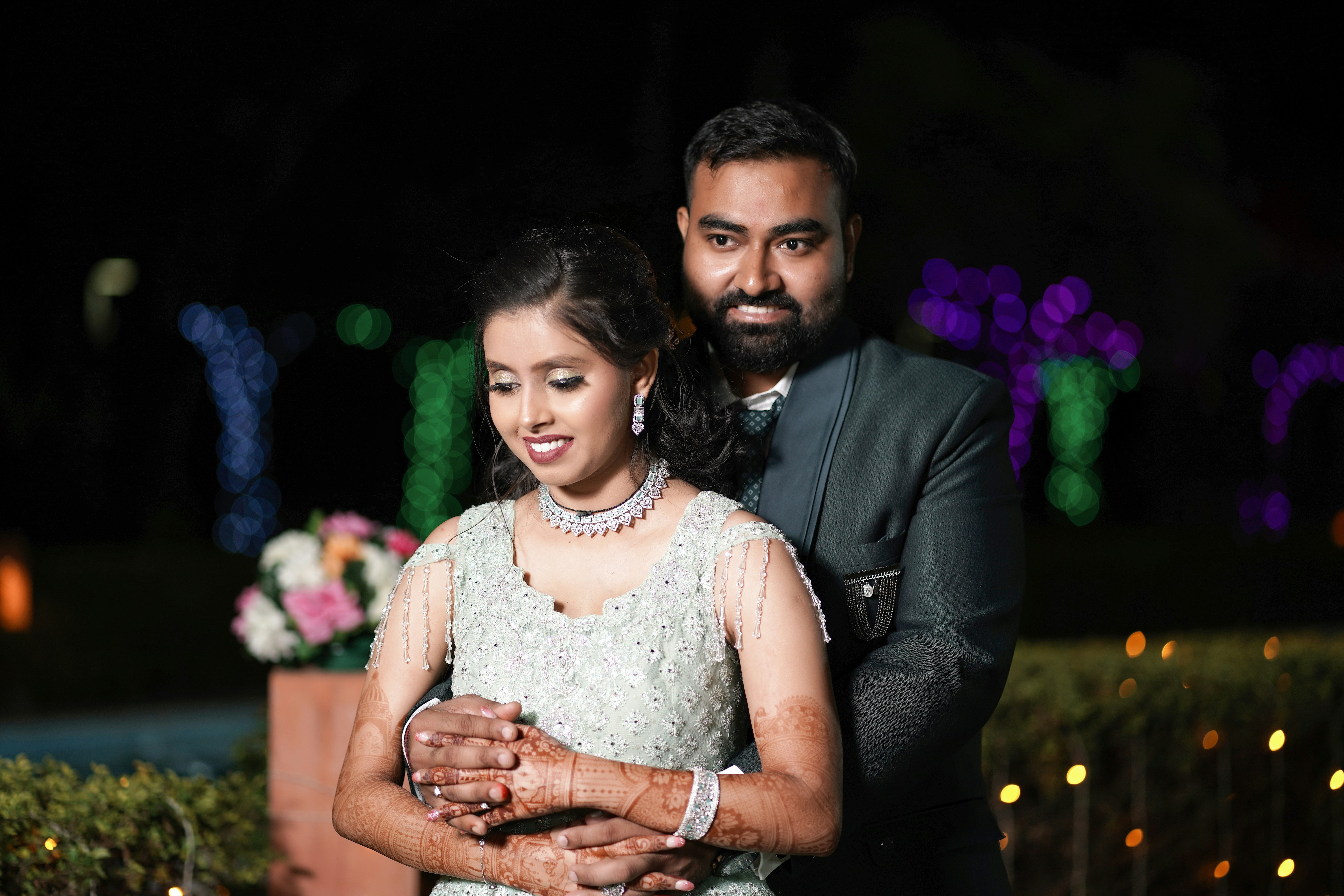Couple in formal attire sharing a tender moment with colorful lights in the background.