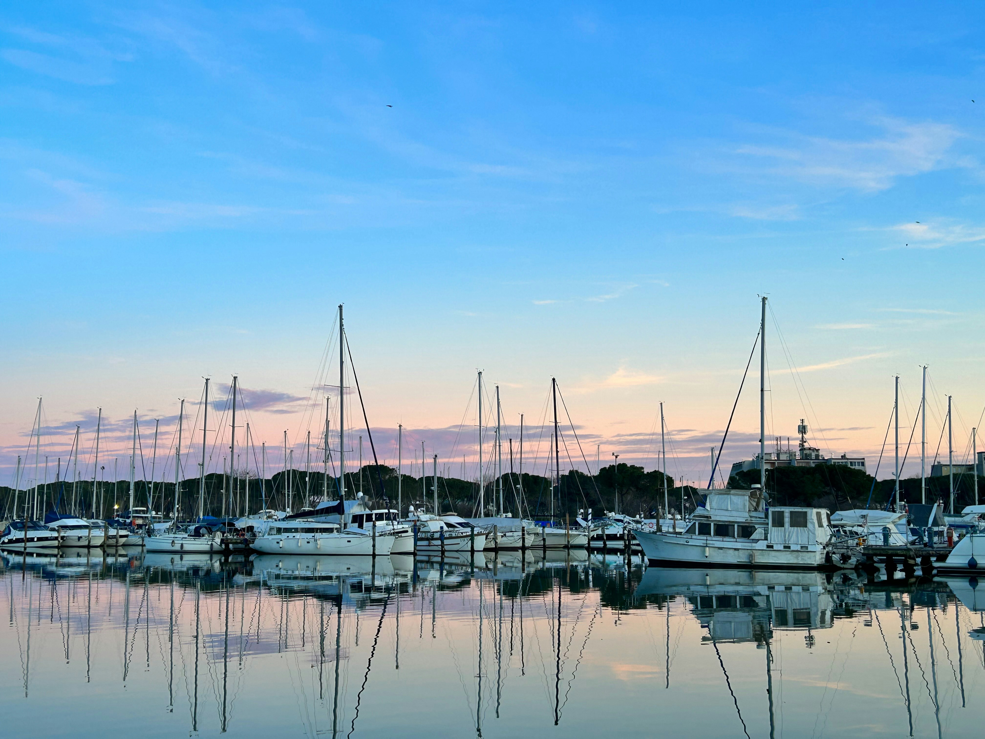 Sailboats and yachts anchored in a serene harbor under a pastel sunset sky.