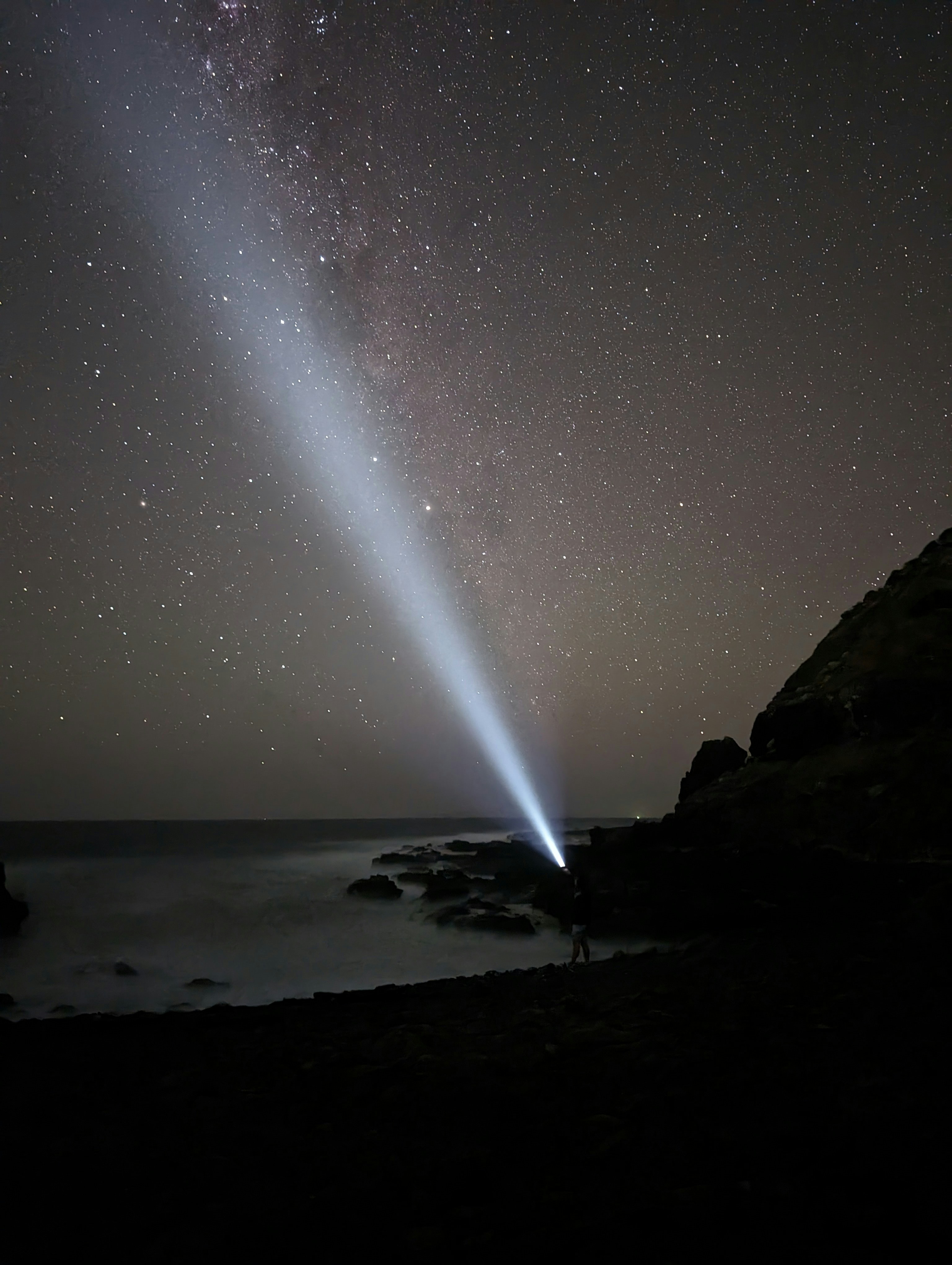 A bright beam of light shines in the night sky over the ocean photo ...