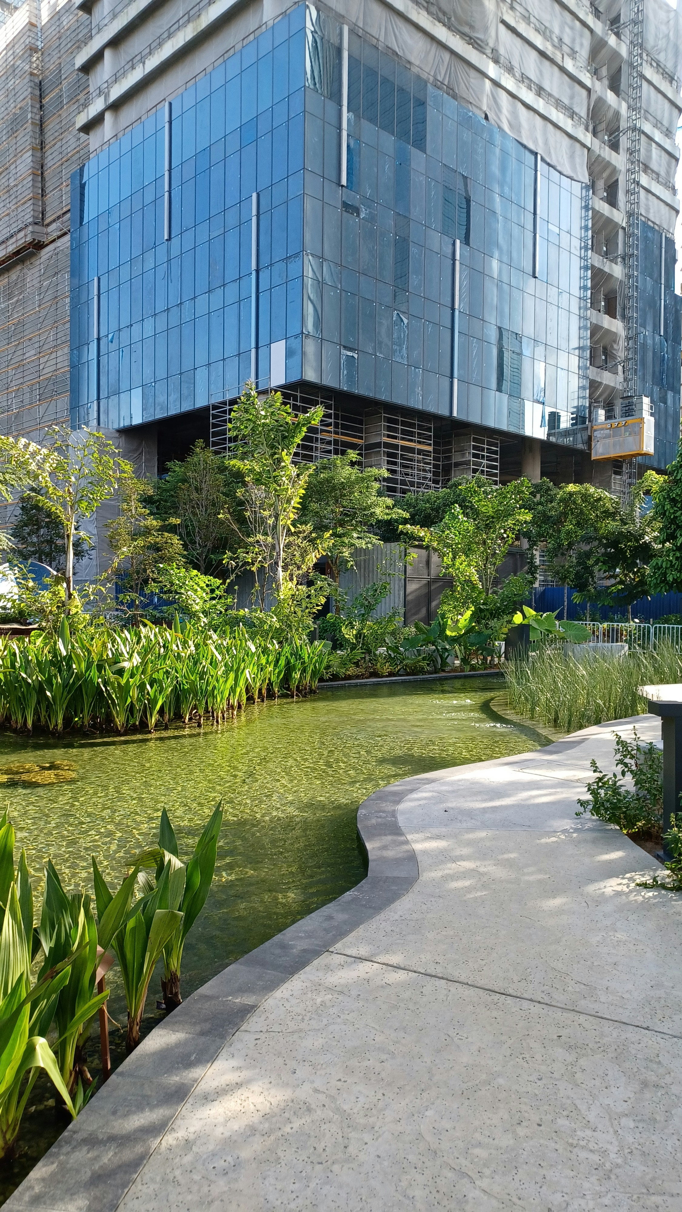Lush greenery surrounds a tranquil waterway, reflecting modern architecture in a vibrant urban landscape.
