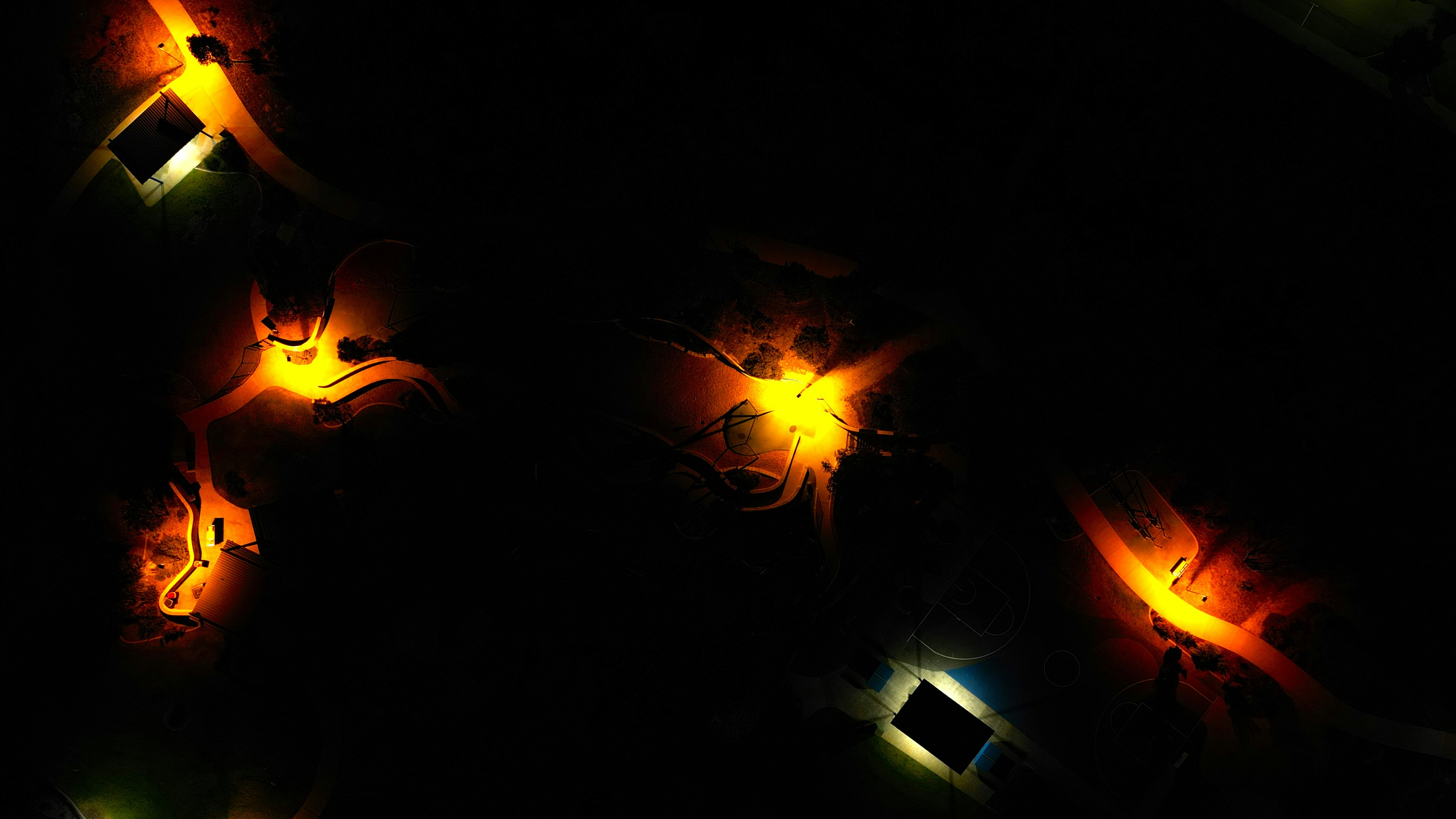 Dark macro scene featuring several orange LED glows illuminating curved metal and plastic components. A glow-dominated composition emphasizing contrast and texture in a minimal setting.