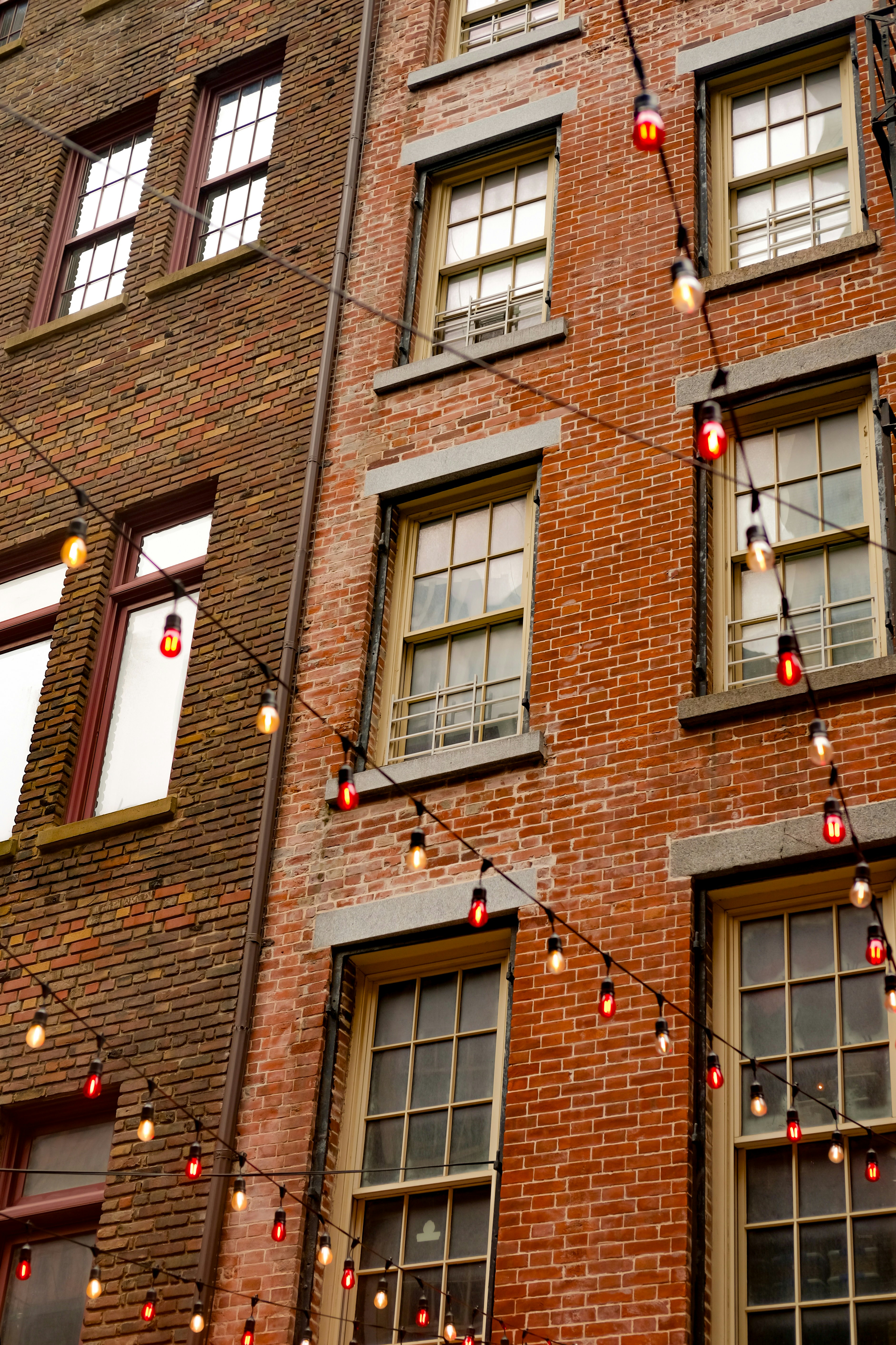 Brick townhouse façade with grid windows. Strings of warm bulbs create a festive glow across the scene.