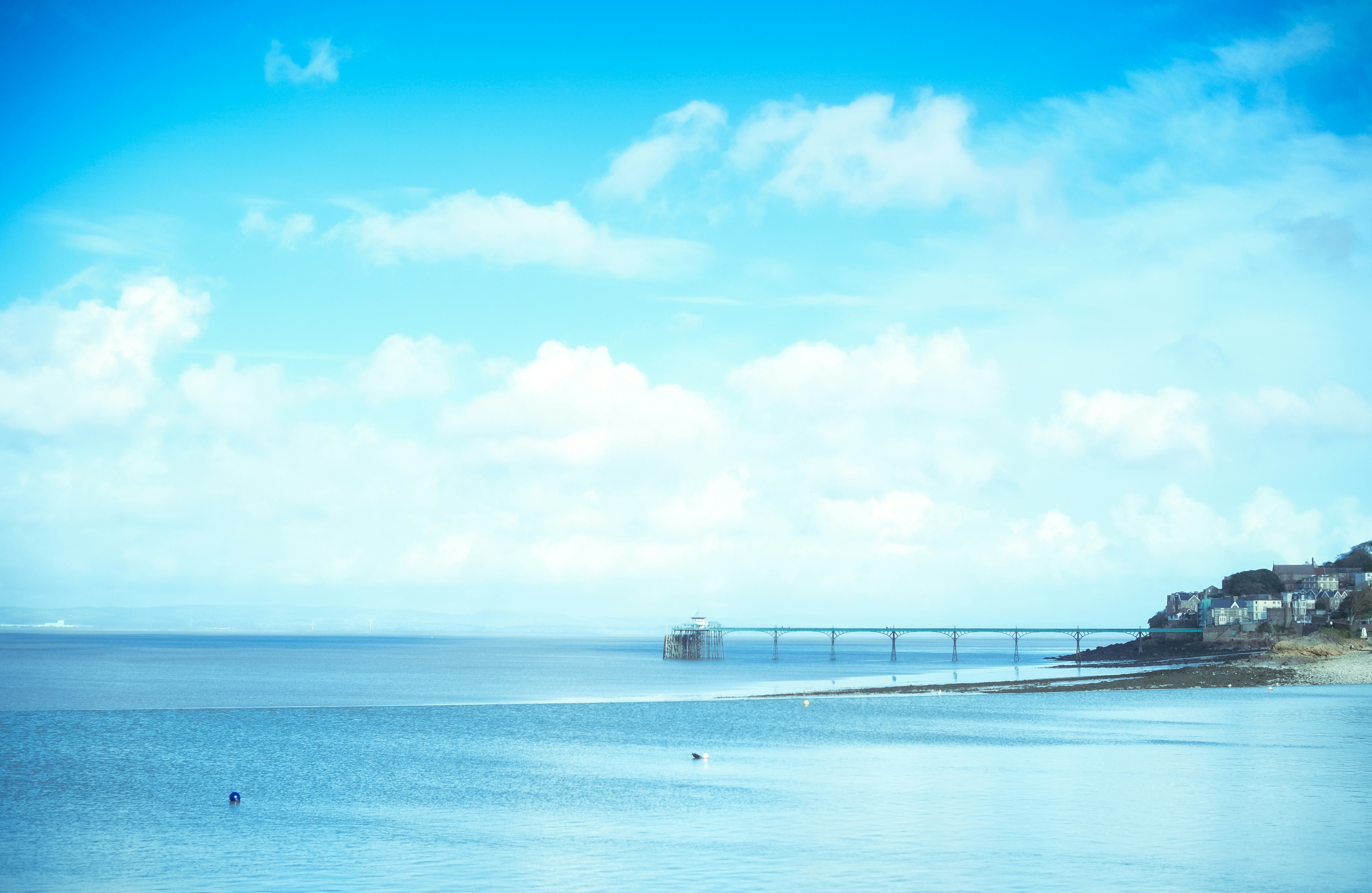 Coastal view with a distant pier extending into the calm sea under a bright blue sky.