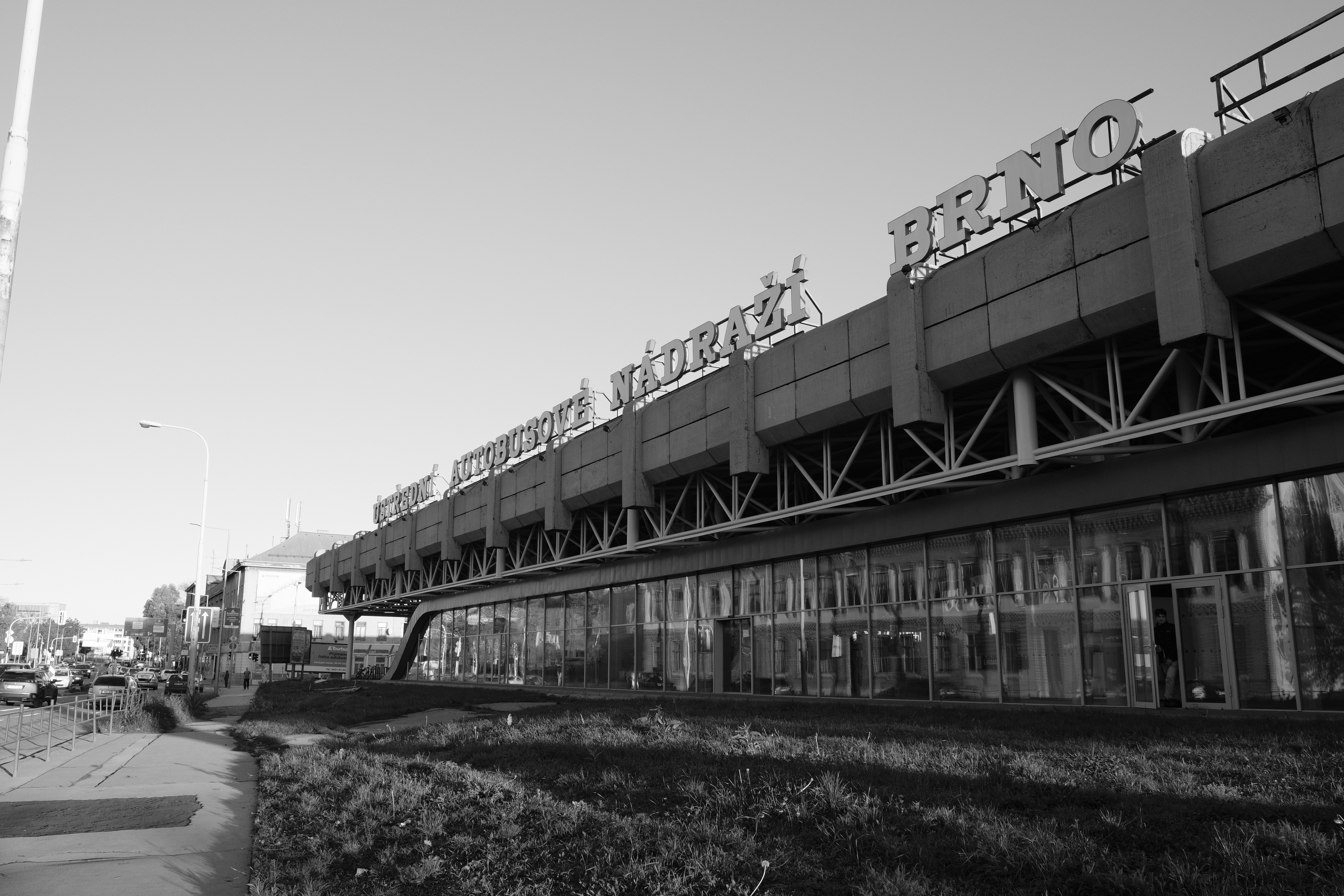 Black and white photograph of a modernist building with prominent signage and glass facade under a clear sky.