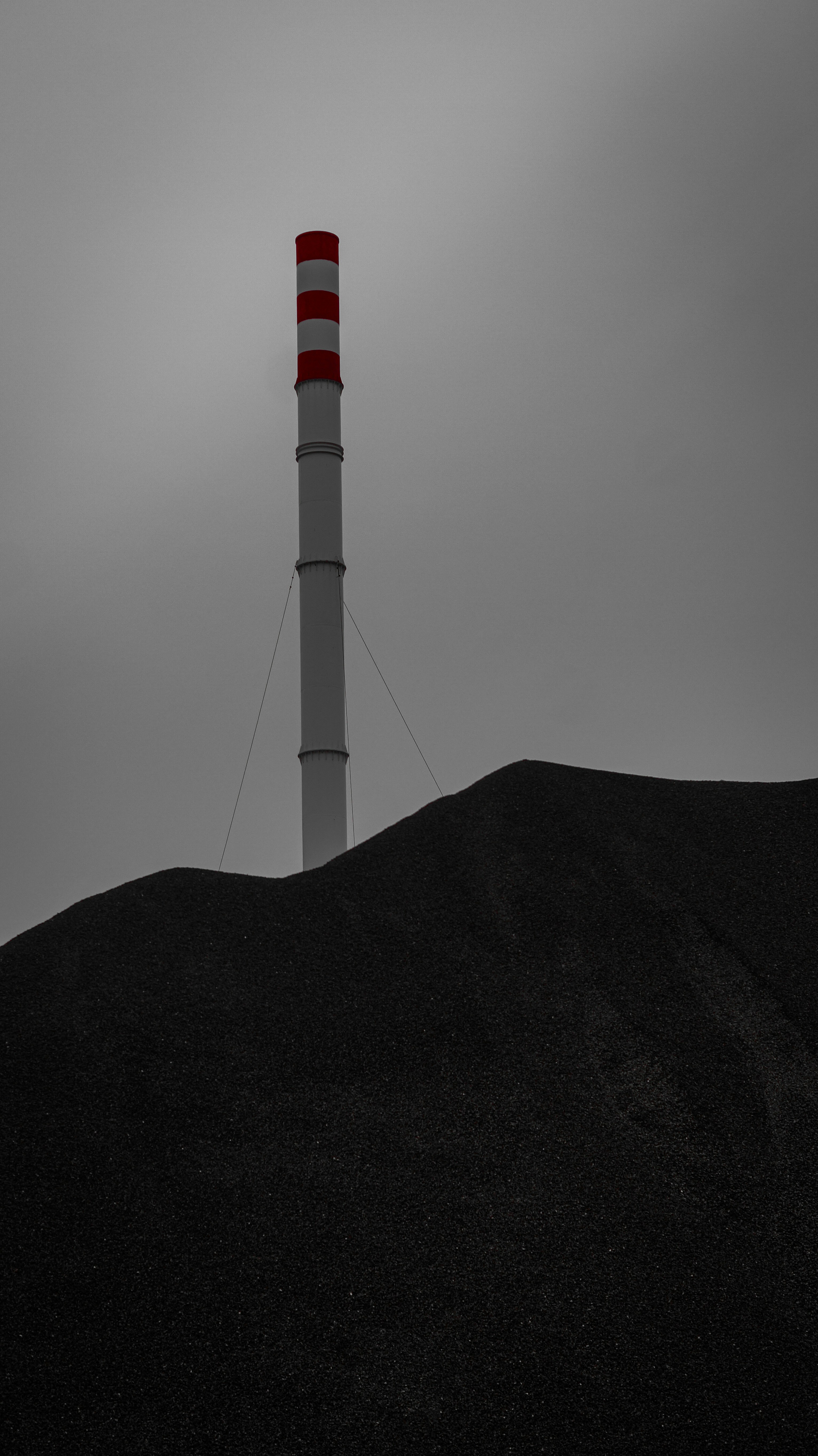 Red-Striped Chimney Rising Over a Coal Heap under a Grim Sky