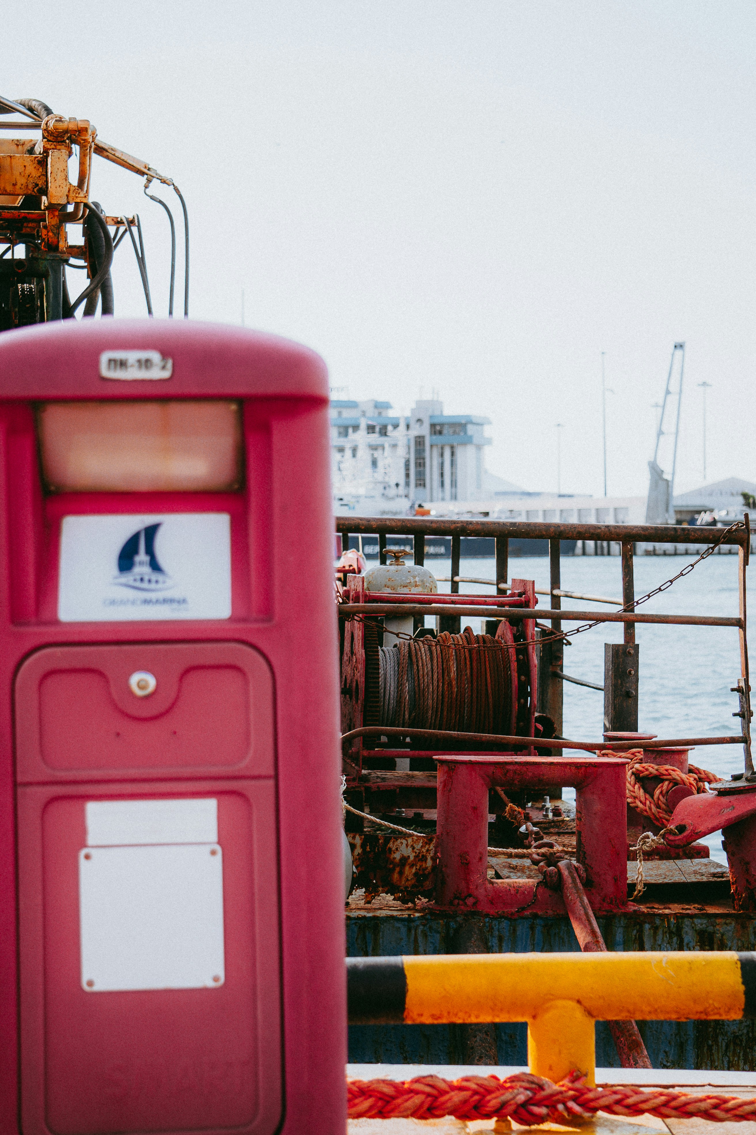 Crimson Dockside: A Pink Telephone Box Against Weathered Rails by the Harbor