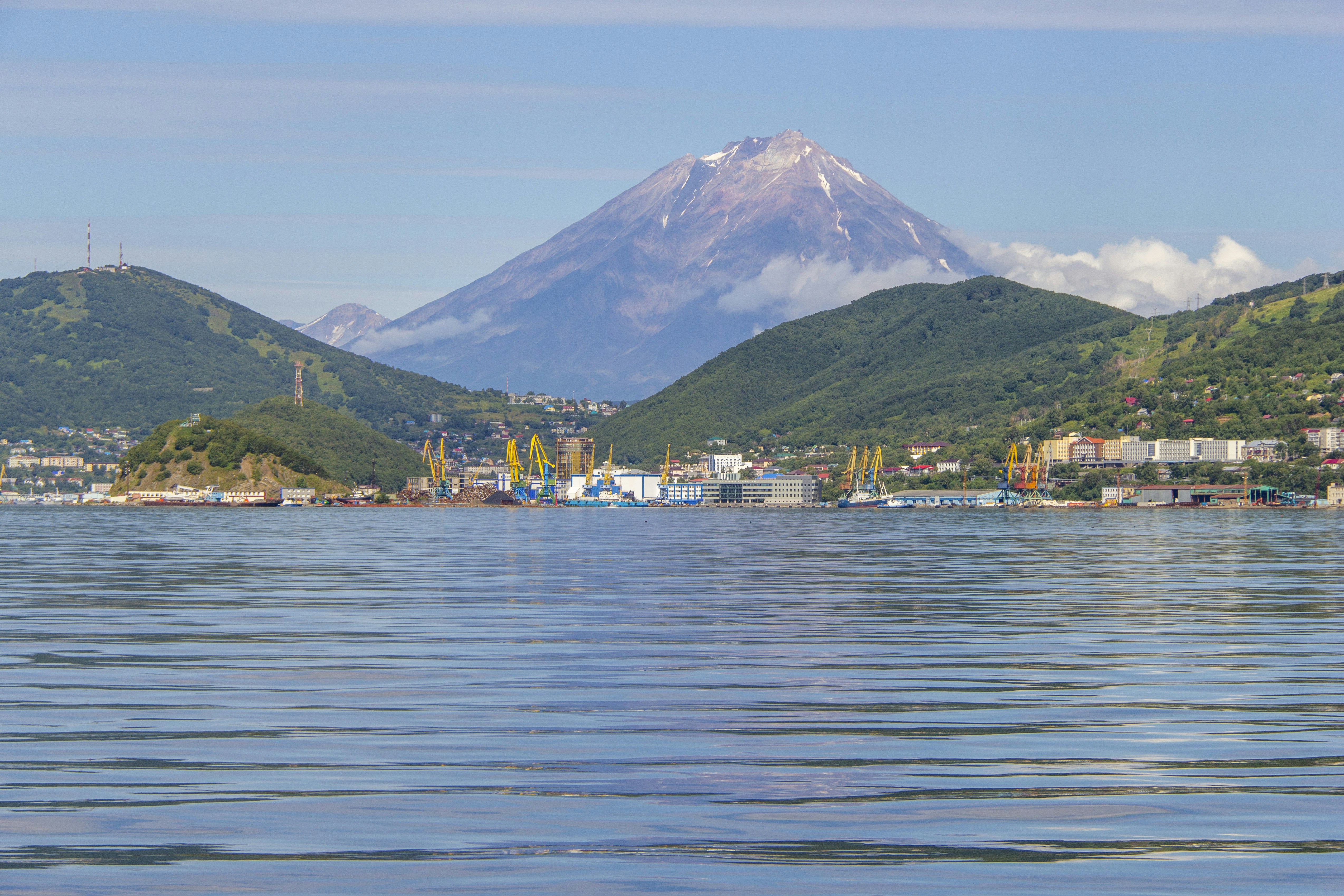 Mountain rising behind a calm body of water with distant hills and scattered clouds.