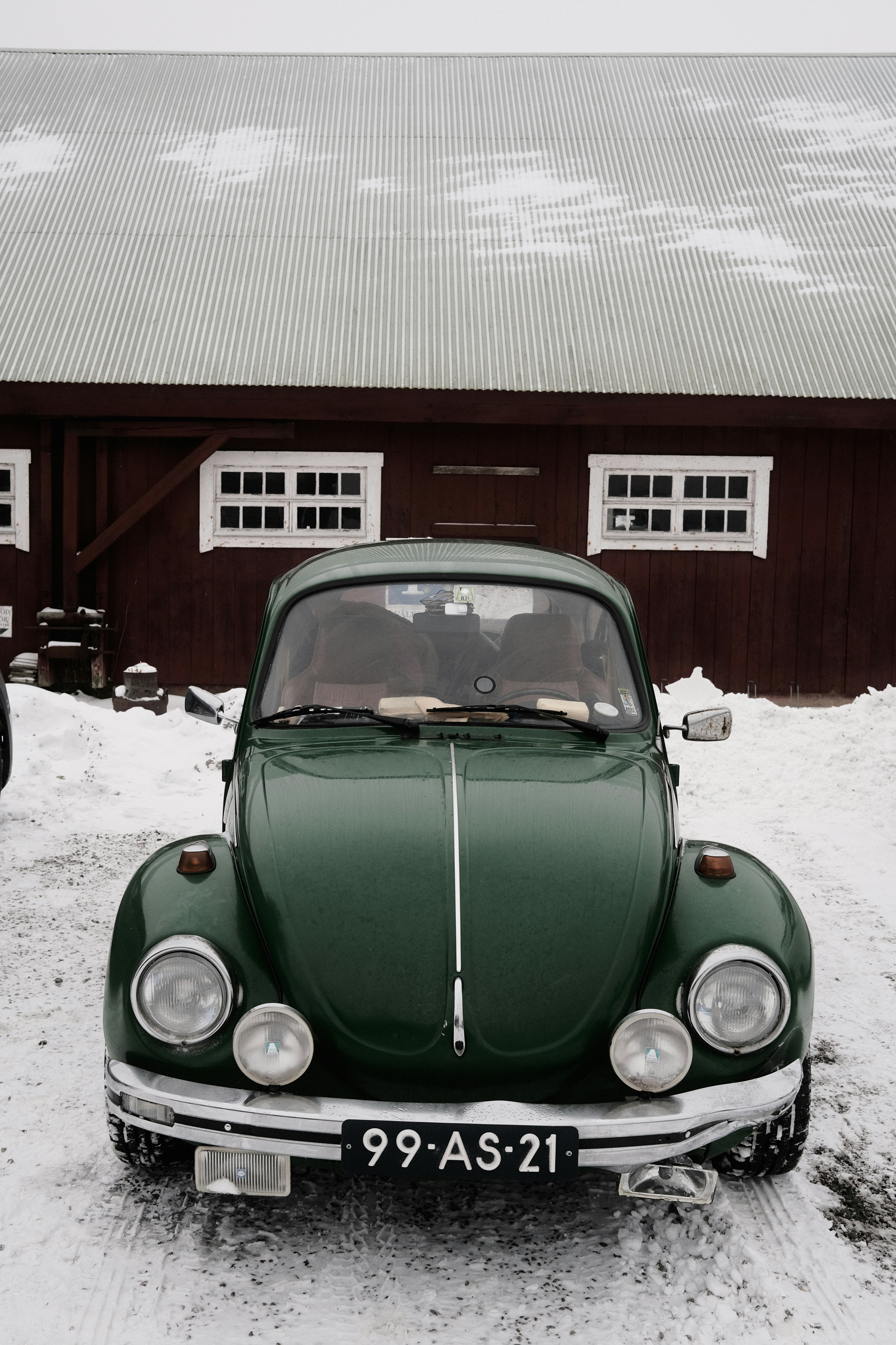 Front-Row Winter Portrait: A Green VW Beetle Before a Red Barn