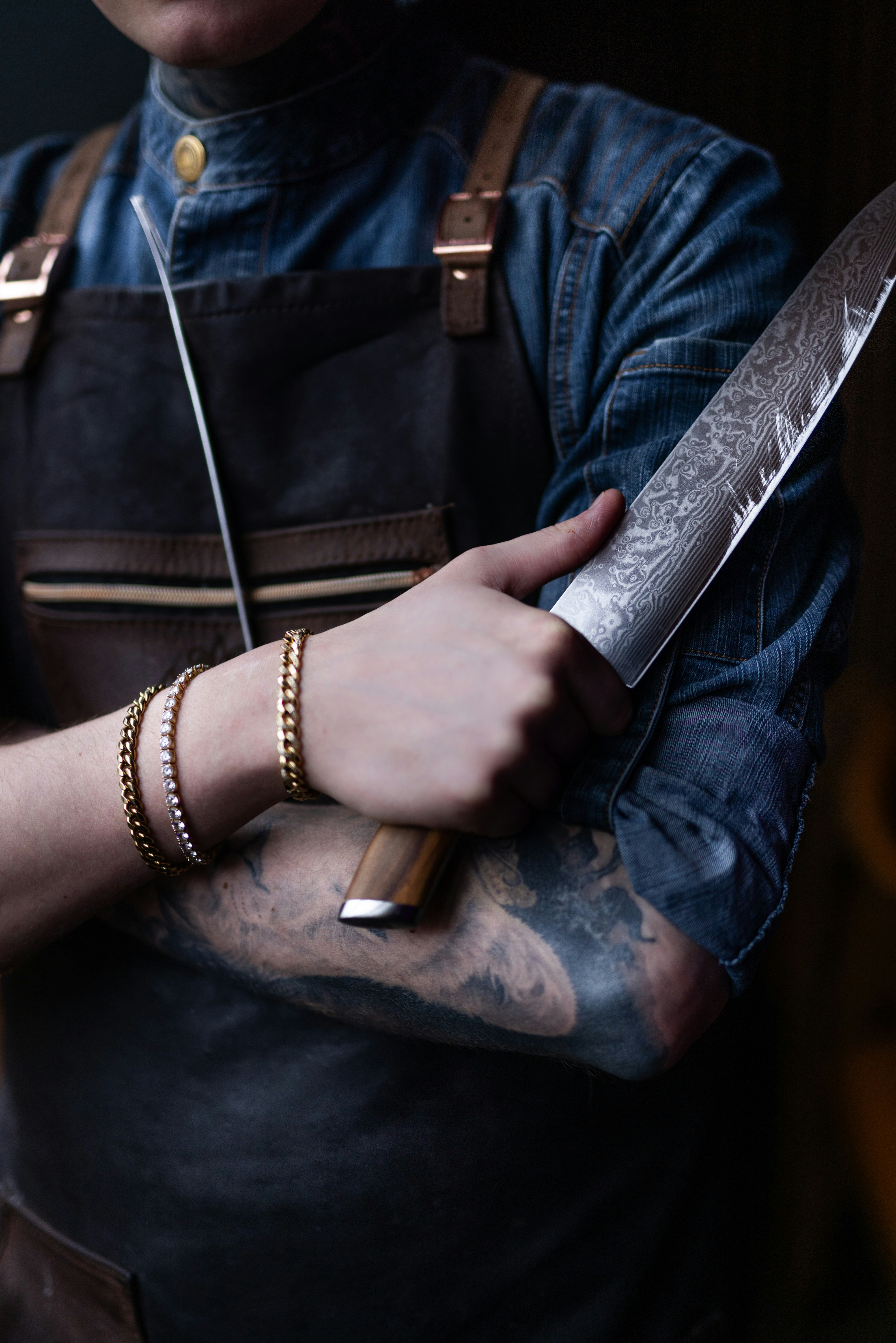 Edge in Focus: Damascus Pattern Knife Gripped by a Tattooed Craftsman