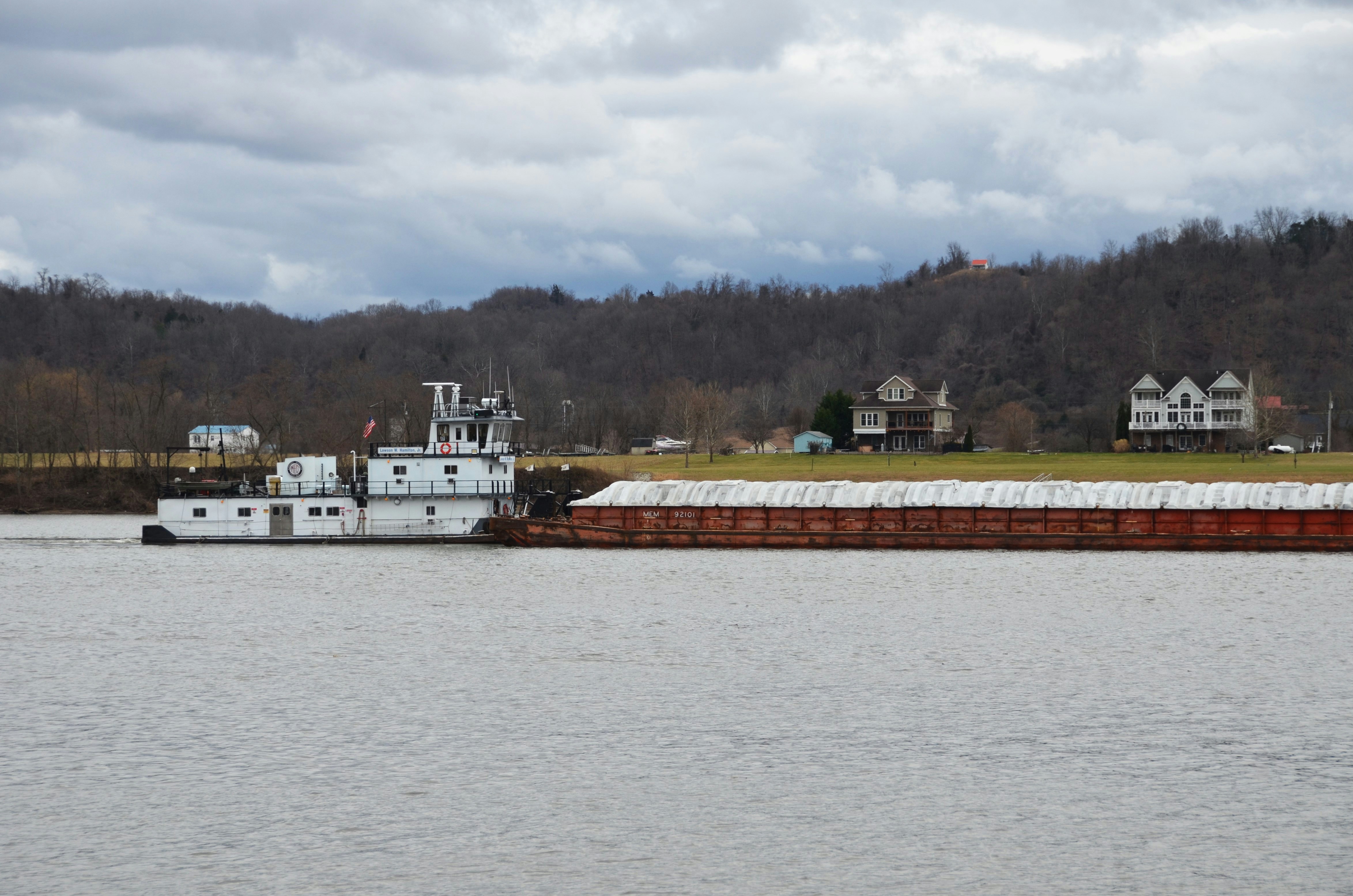 White Tug at the River's Edge, Framing a Rust-Red Barge Beneath a Quiet Hillside