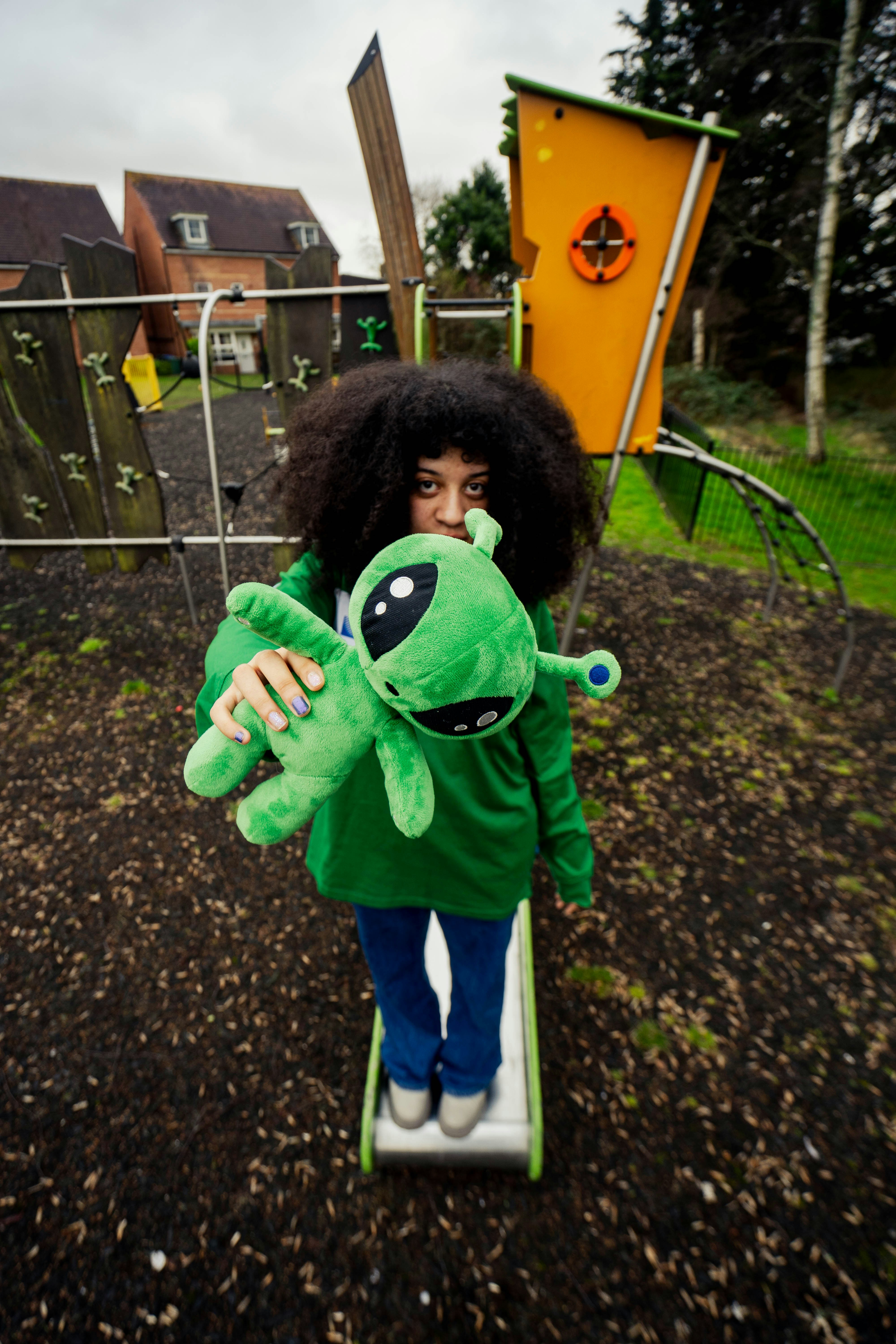 Green Hello: A Child with a Plush Alien on a Playground Ride