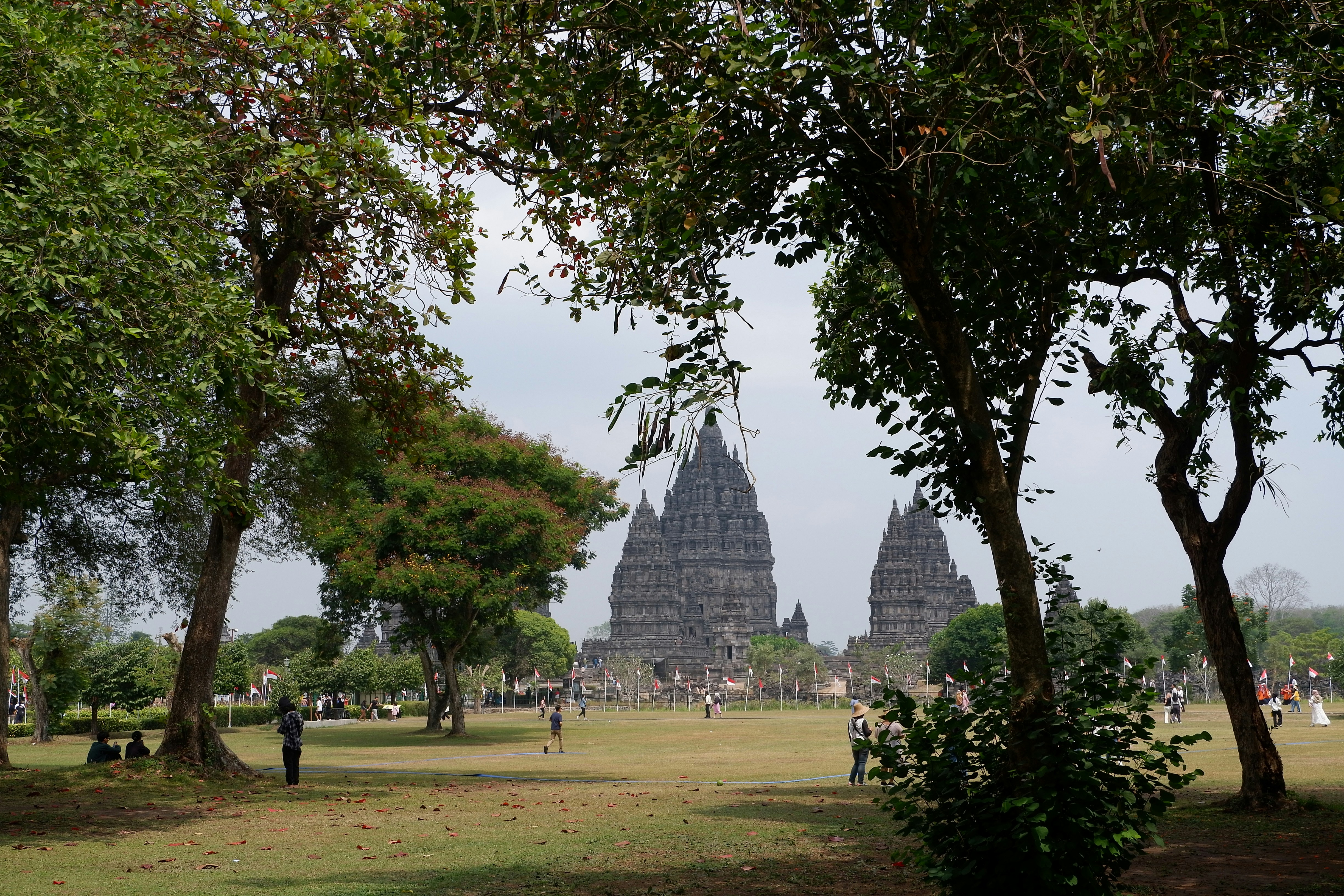 Park lawn frames distant ancient temple spires beneath a cloudy sky as visitors wander the open grounds. This landscape photograph emphasizes serene scale and heritage.