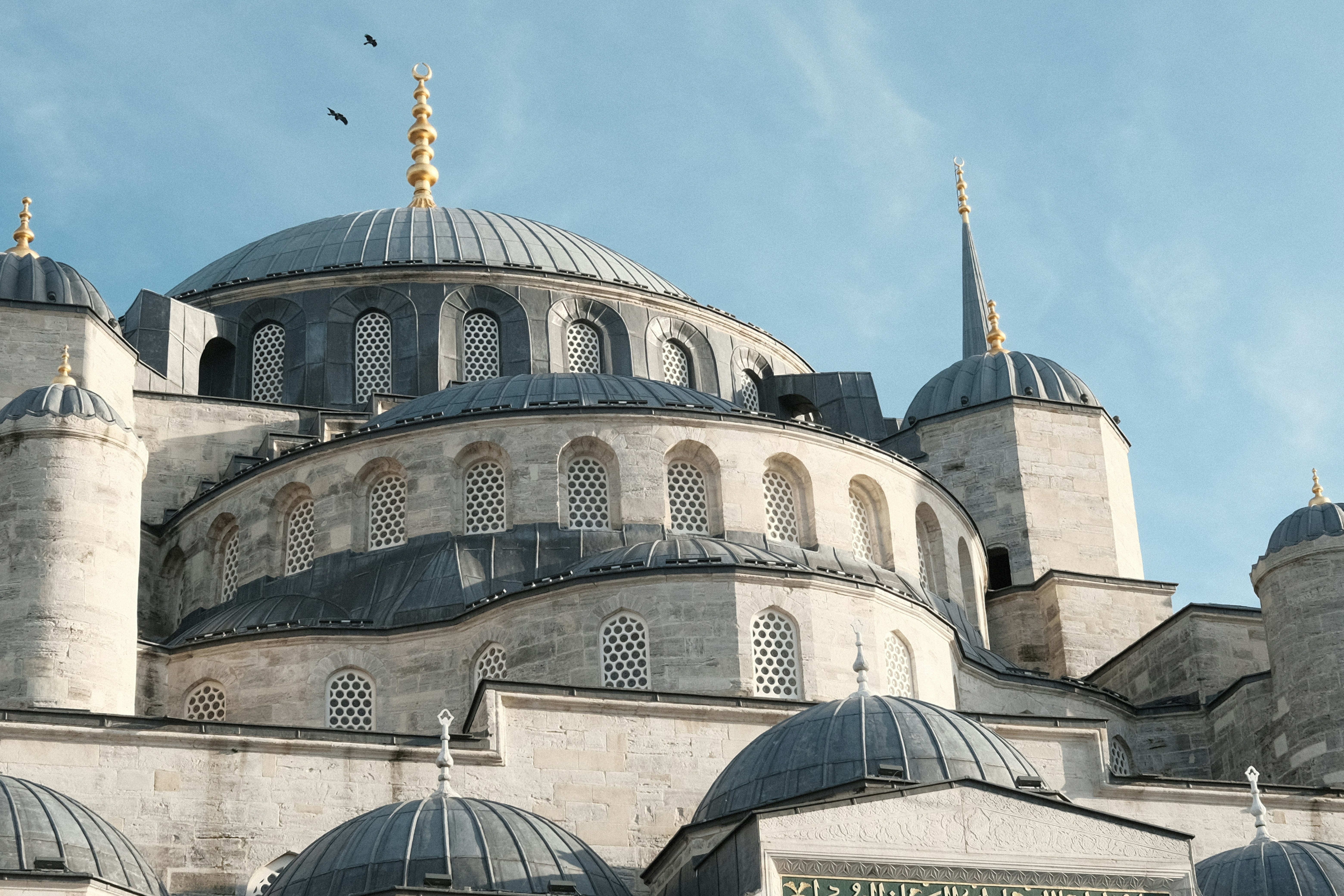 Ornate domes and spires of an ancient stone building against a bright blue sky.