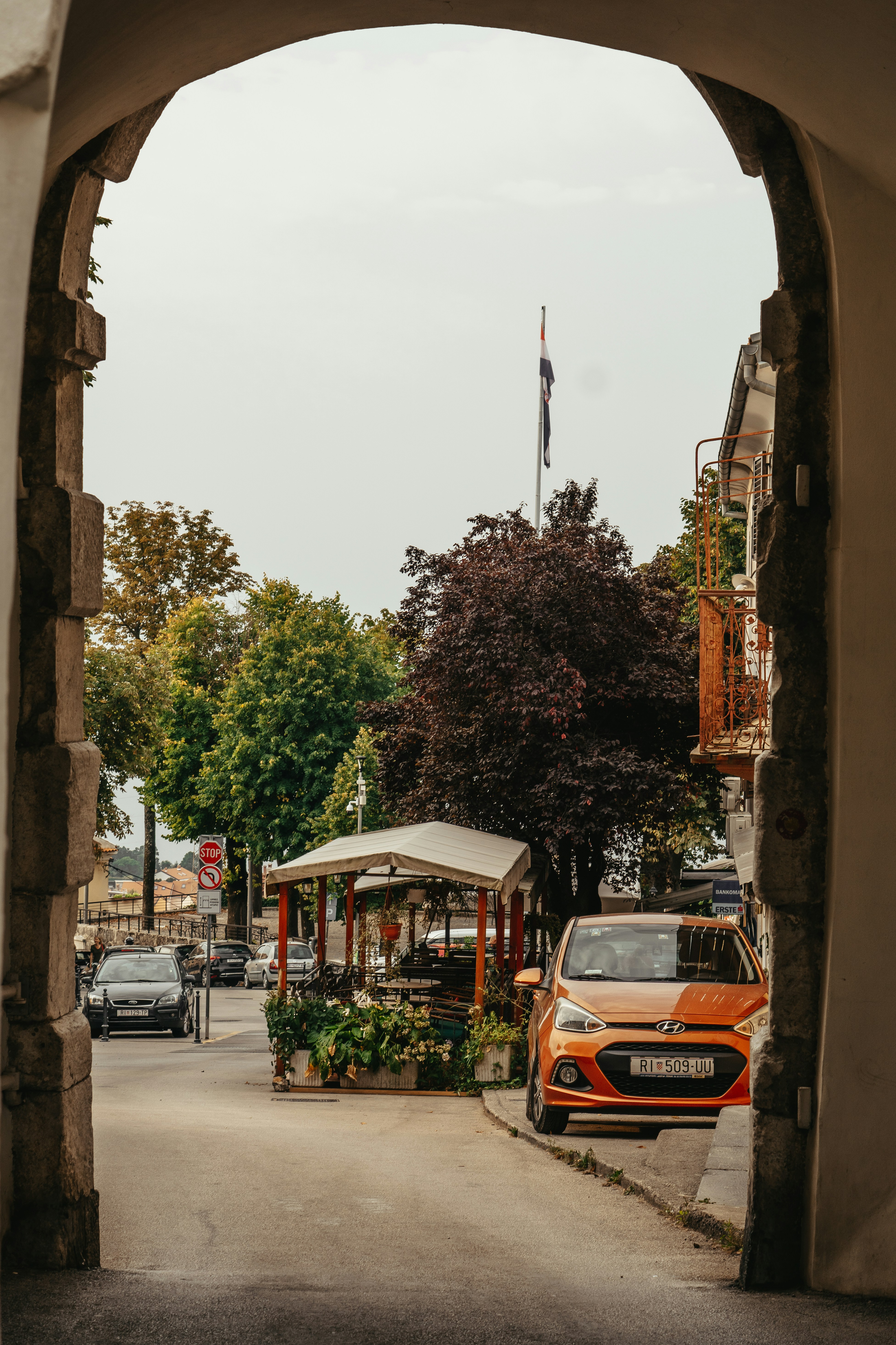 Archway View: Sunlit Street, Market Stall, and an Orange Hyundai