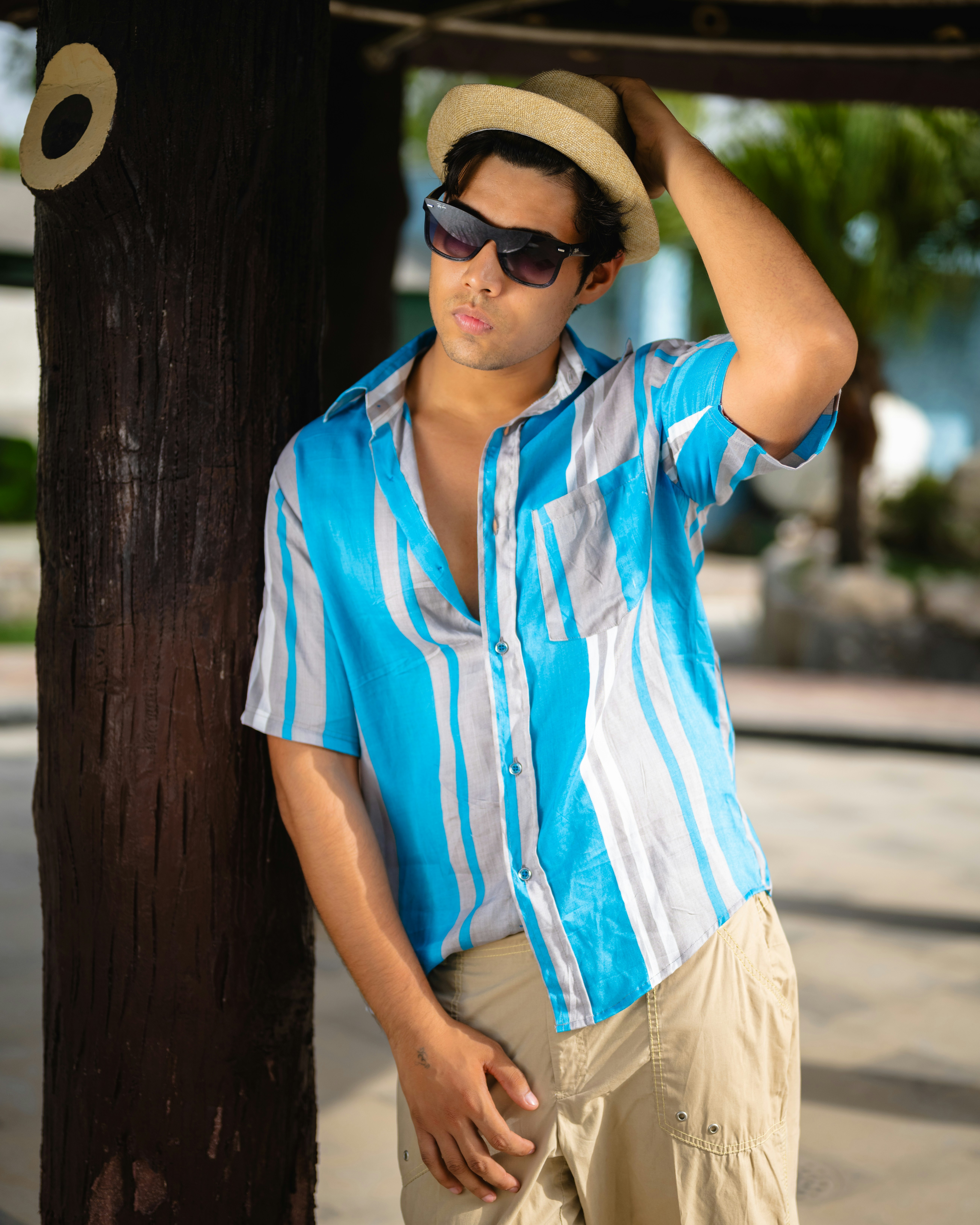 a man in a hat and sunglasses leaning against a tree