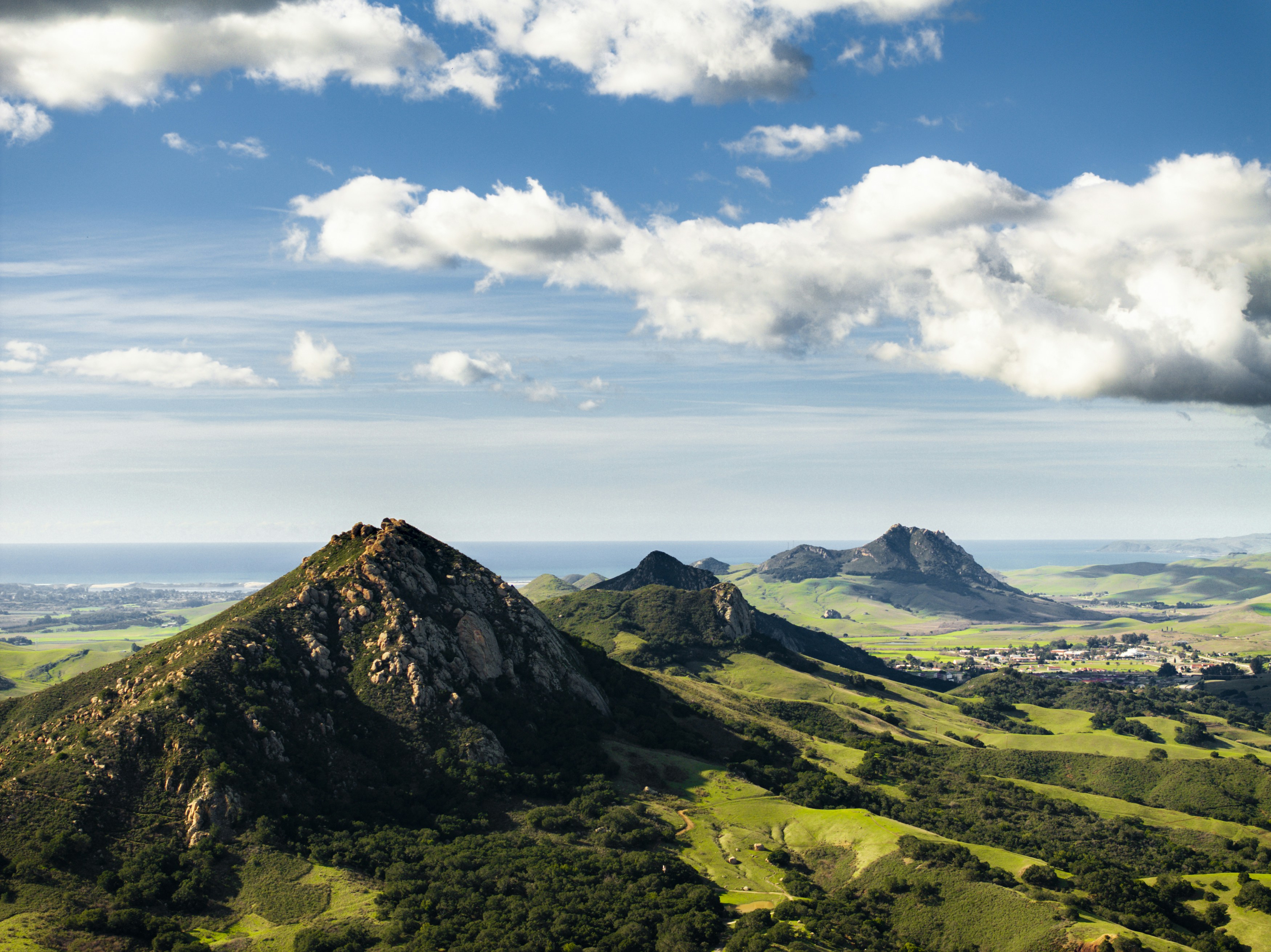 Rolling green hills and distinct mountain peaks under a sky dotted with clouds.