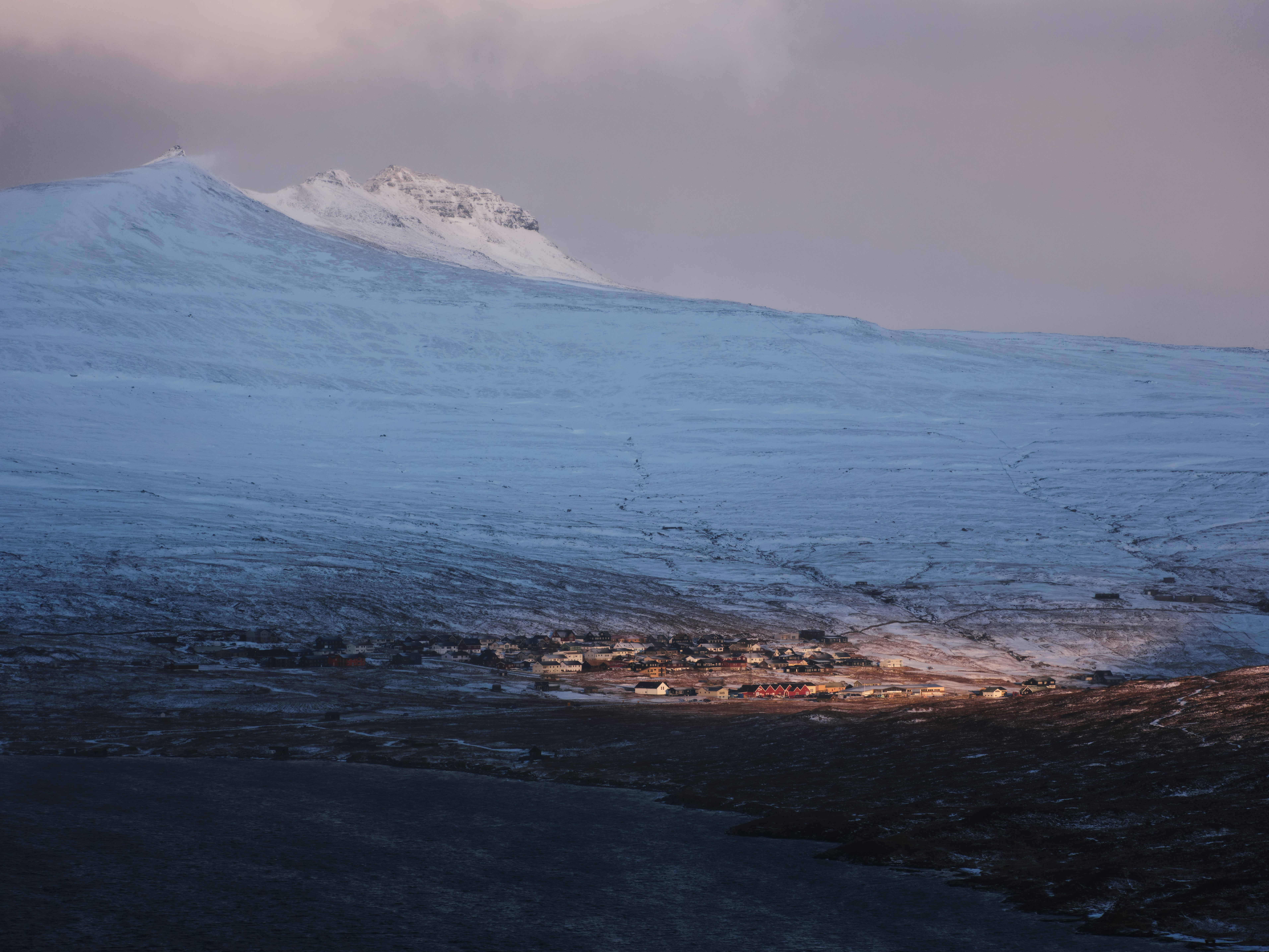 A snow covered mountain with a small village below photo – Free Vágar ...