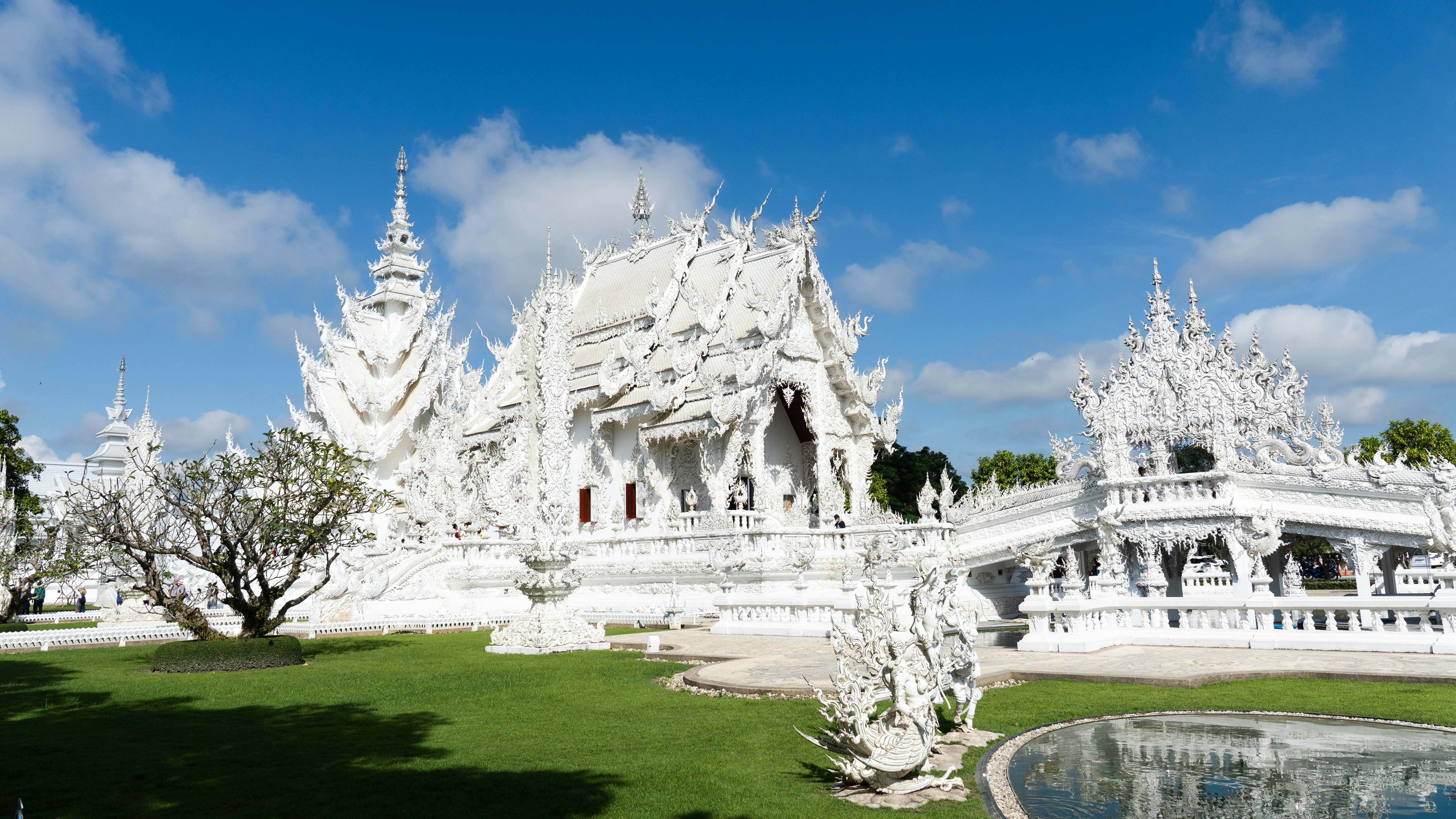 Intricate white temple with ornate details set against a bright blue sky and lush greenery.