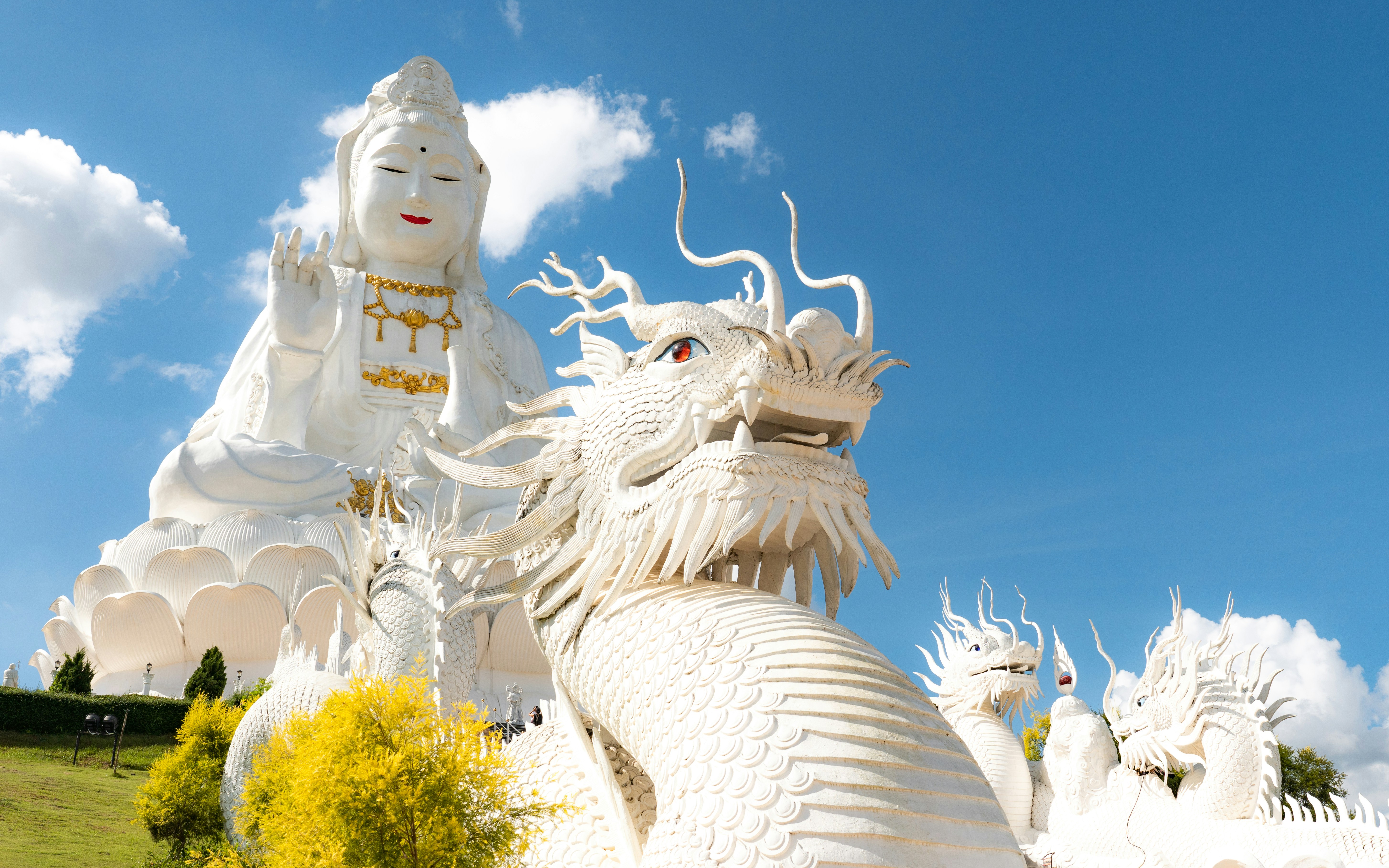 White dragon statue with intricate scales against a bright blue sky and clouds.