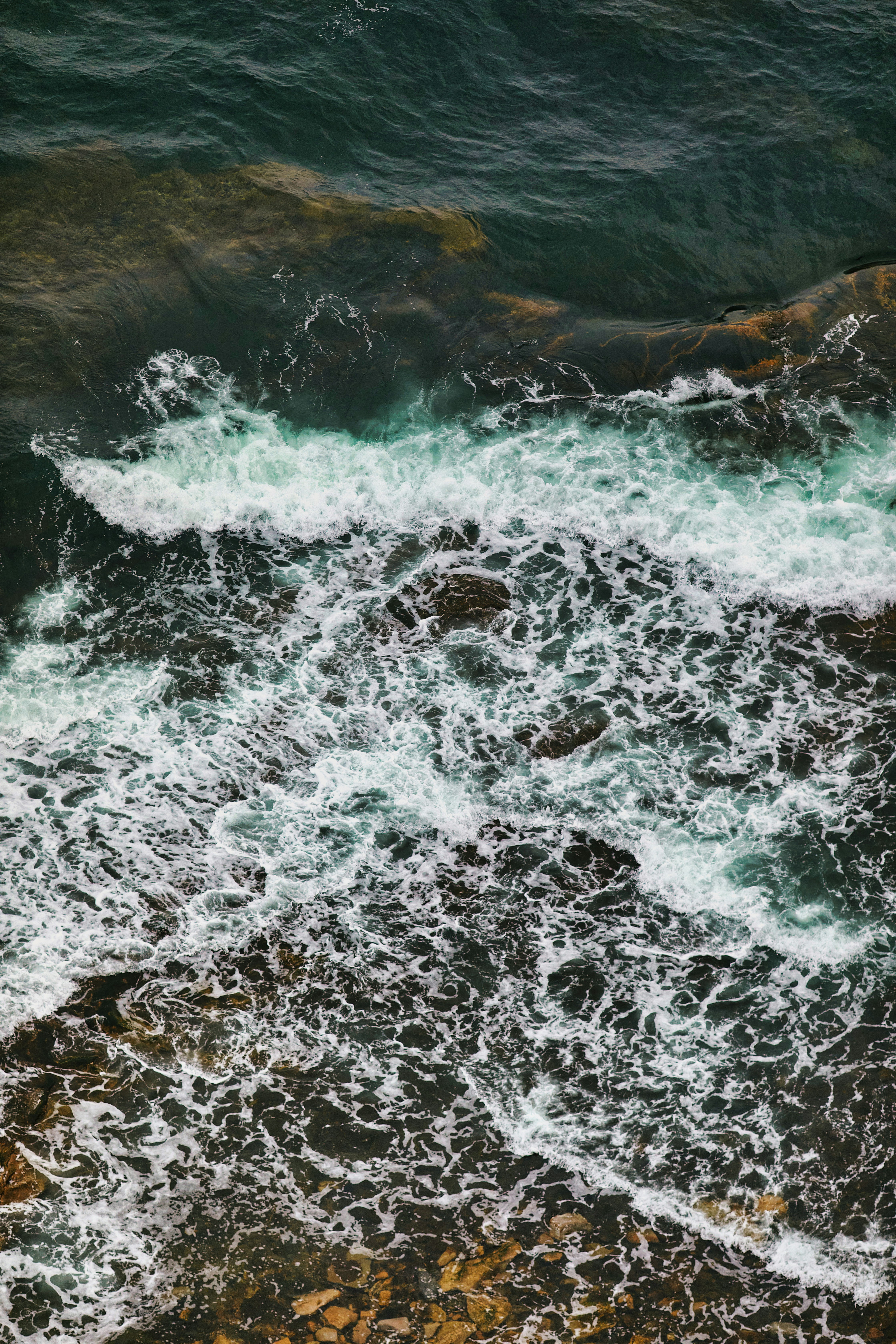 Waves crashing over a rocky shoreline with white foam and greenish-blue water.