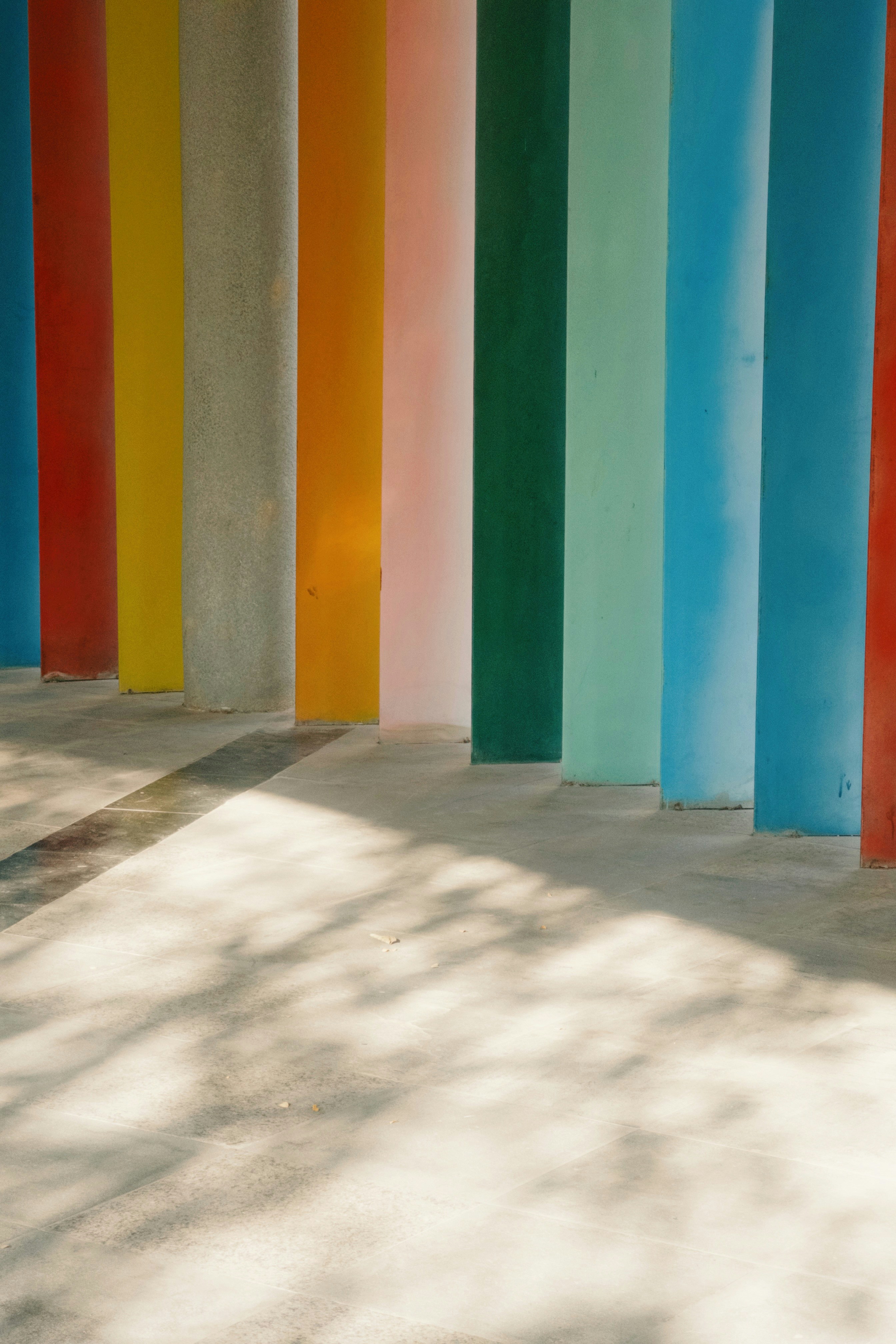Rainbow Columns in Shade: A Row of Painted Pillars Casting Soft Shadows