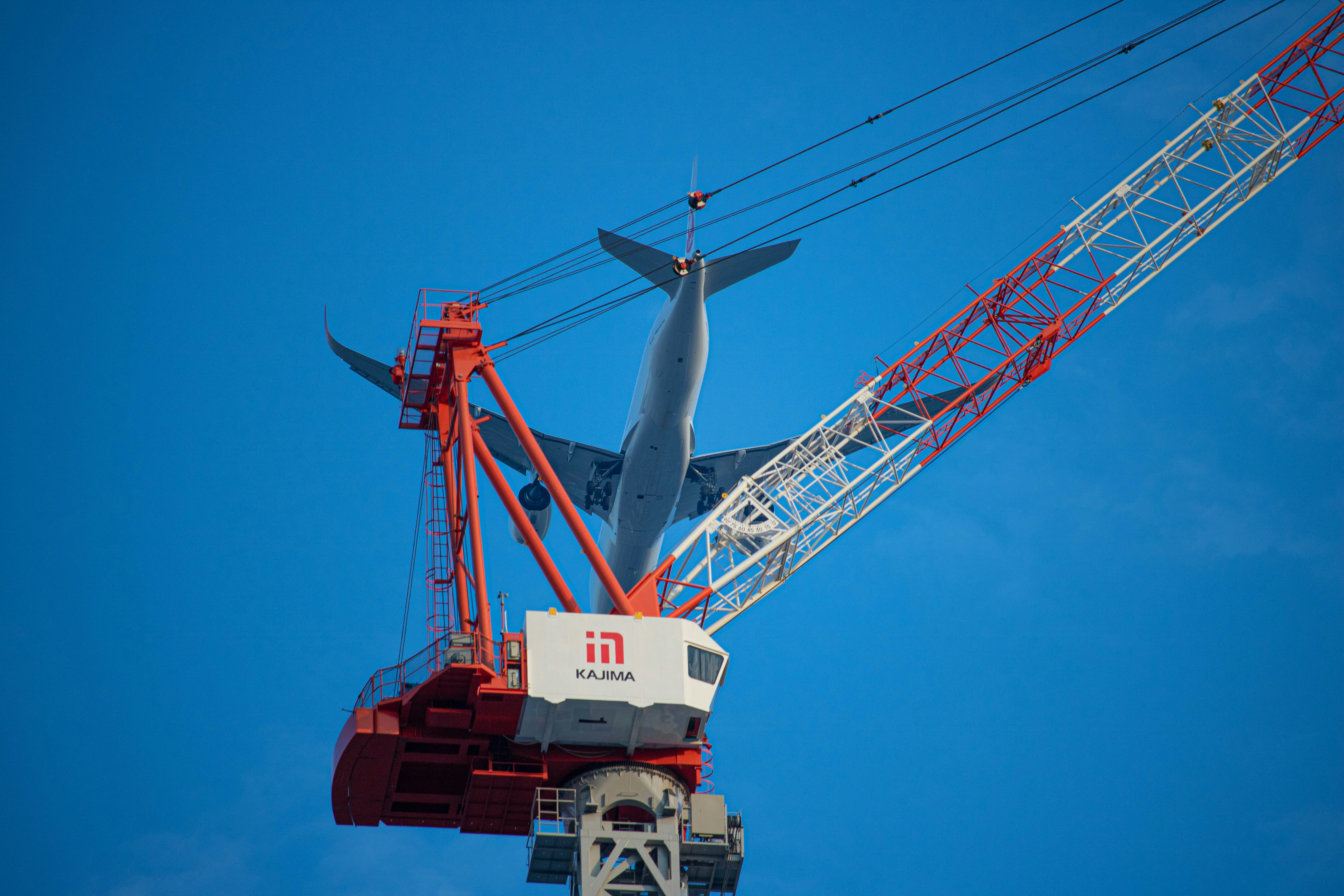 Tower crane with a small airplane perched at its summit against a clear blue sky.