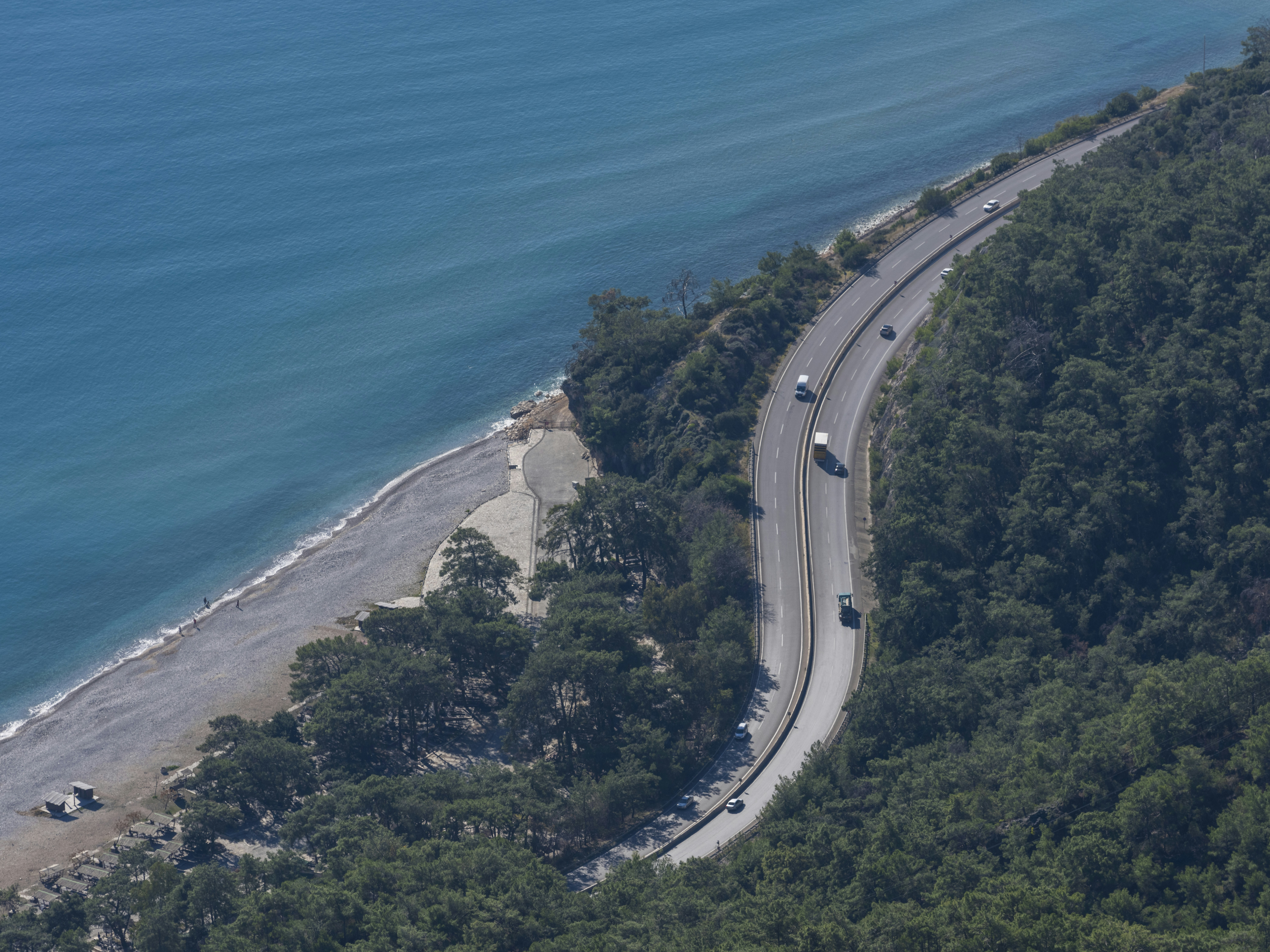 Curved road along a lush forested coastline with vibrant blue waters.
