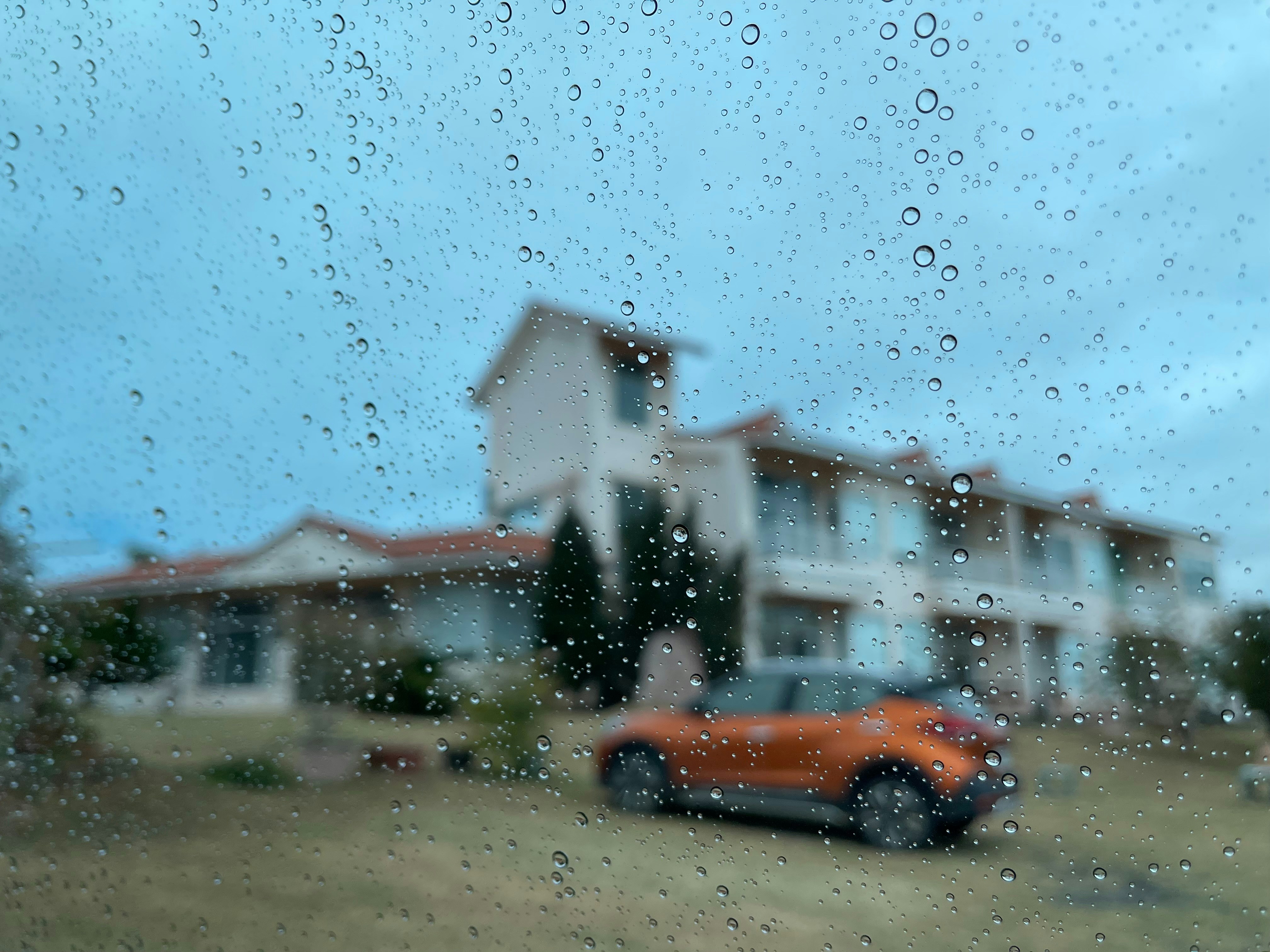 Rain on Glass: An Orange SUV Framed by a Veiled Suburban Driveway