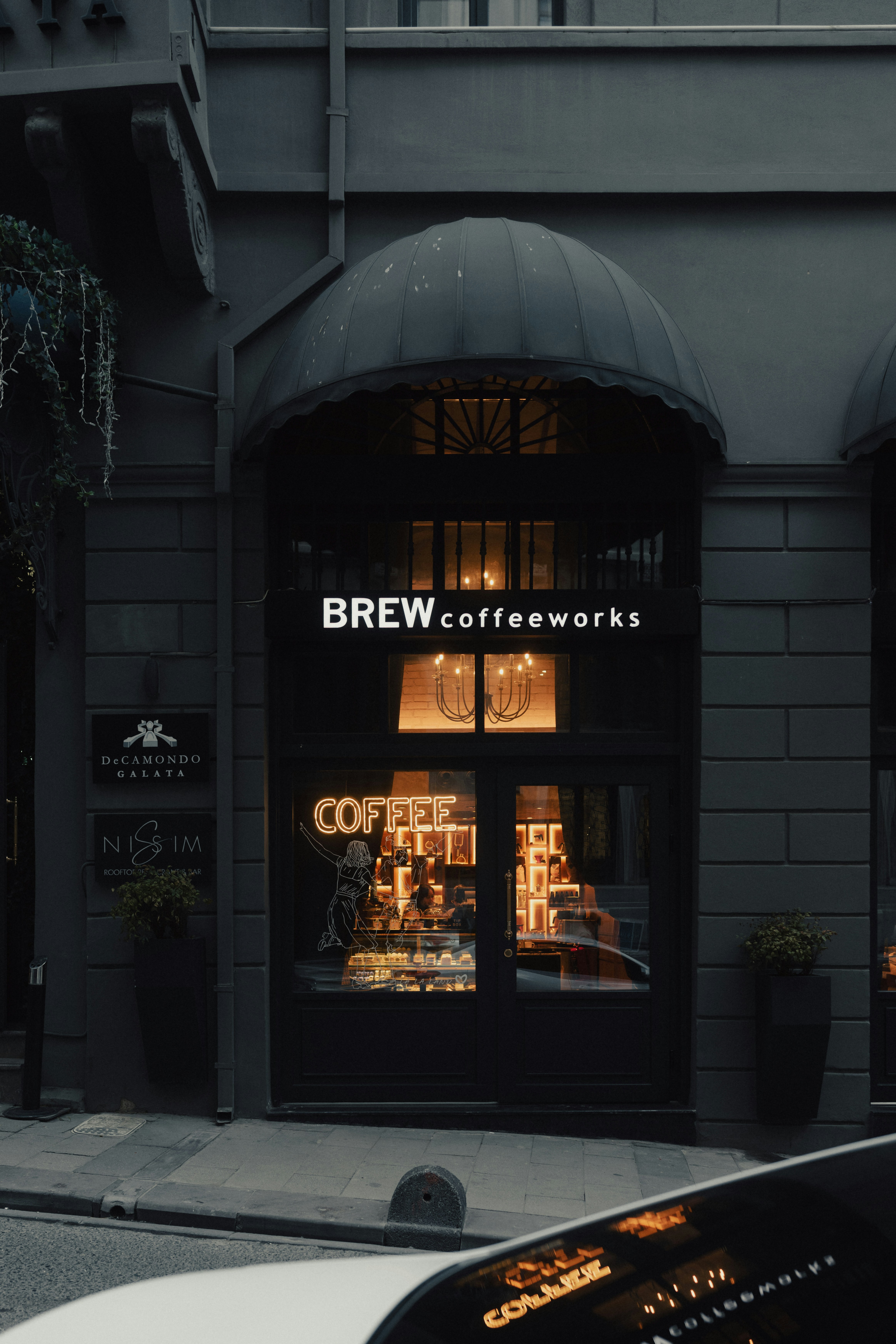 Brew Coffeeworks storefront at dusk, with a warm interior glow visible through glazed doors and a neon COFFEE sign.