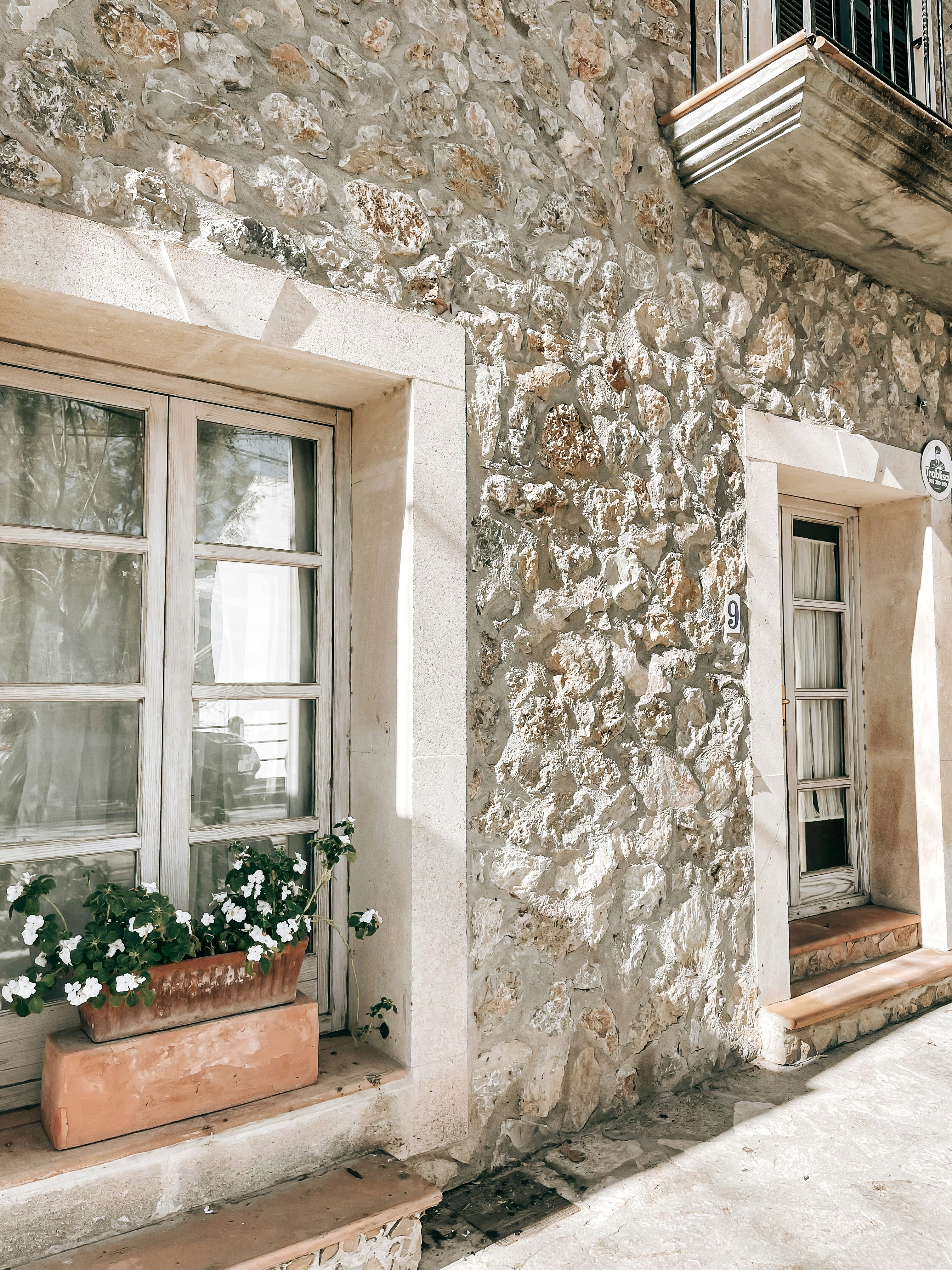 Stone facade with two windows adorned by a terracotta planter filled with white flowers.