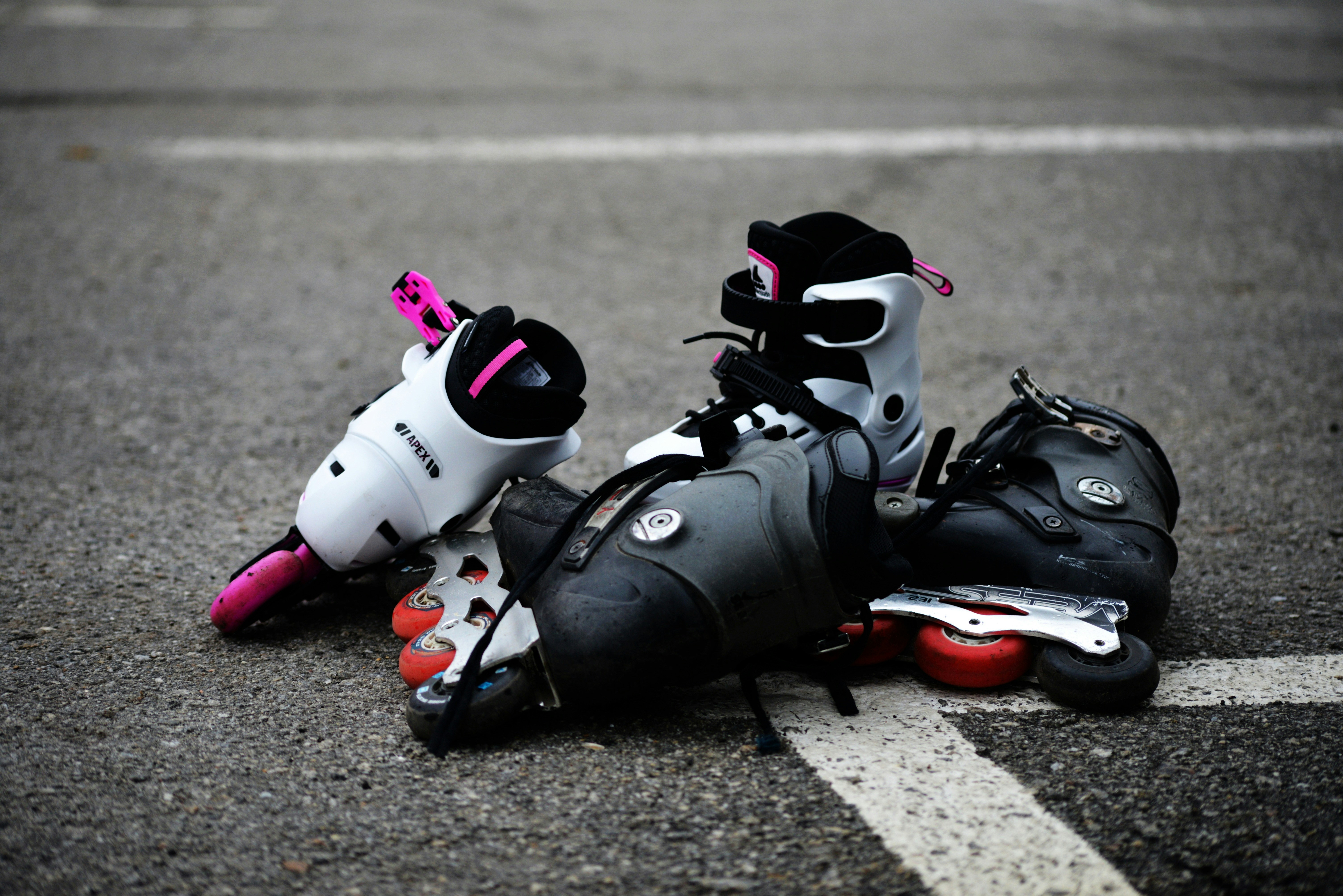 A pile of inline skates rests on a marked parking-line on asphalt in daylight.
