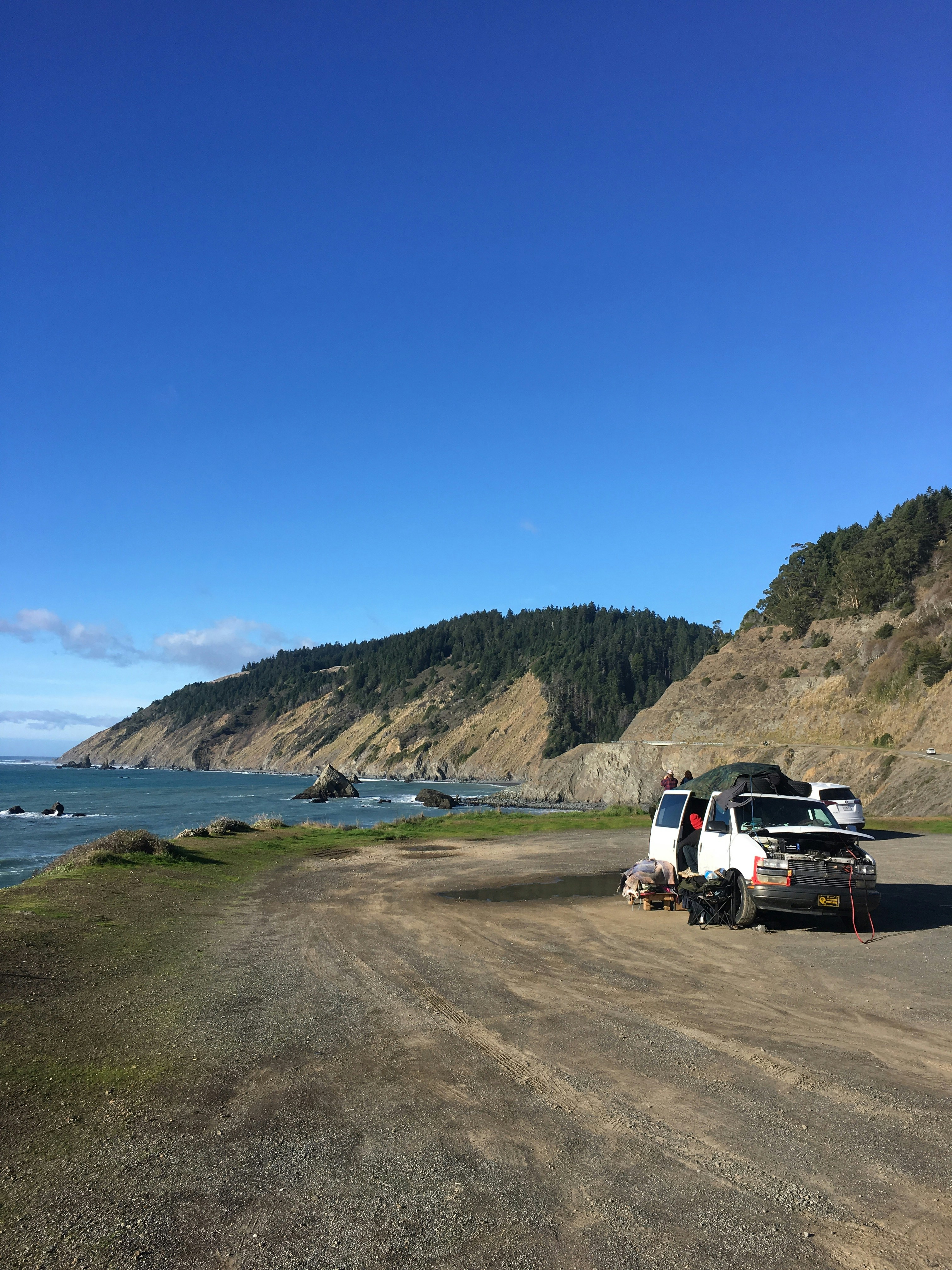 Pictured here is a camper van parked against the backdrop of the Pacific Ocean. This photograph was taken at a scenic vista point just off the northern start of California State Route 1, the most scenic coastal highway in the United States. This northern section of Highway 1 winds through the picturesque coastal region of Mendocino County, characterized by towering redwood forests, rugged cliffs, and panoramic ocean views. The route passes through charming coastal towns such as Fort Bragg and Mendocino, offering travelers a glimpse of California's pristine natural beauty.
