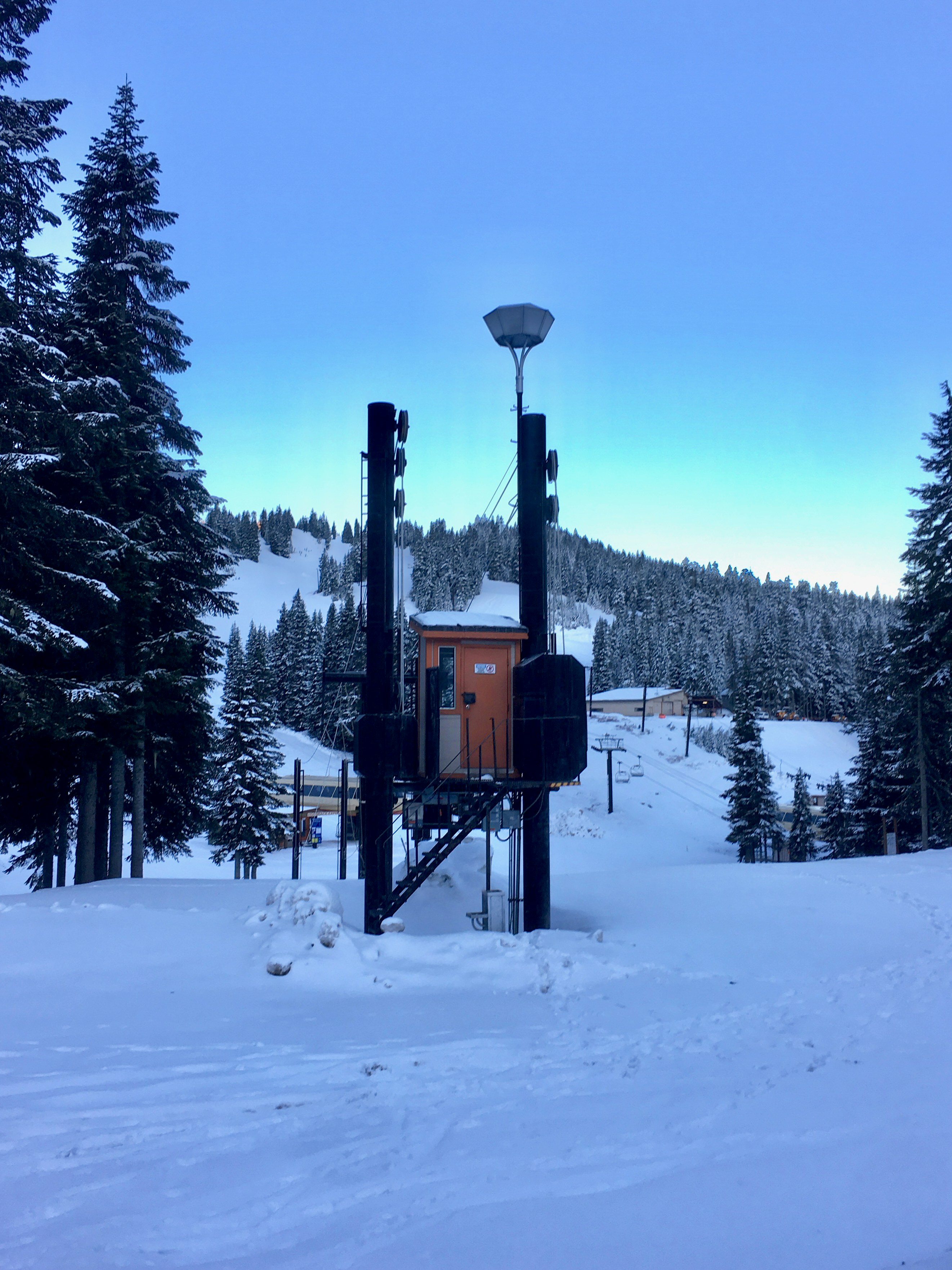 Orange Telecom Hut on a Snowy Steel Pedestal Against a Pine-Draped Ridge