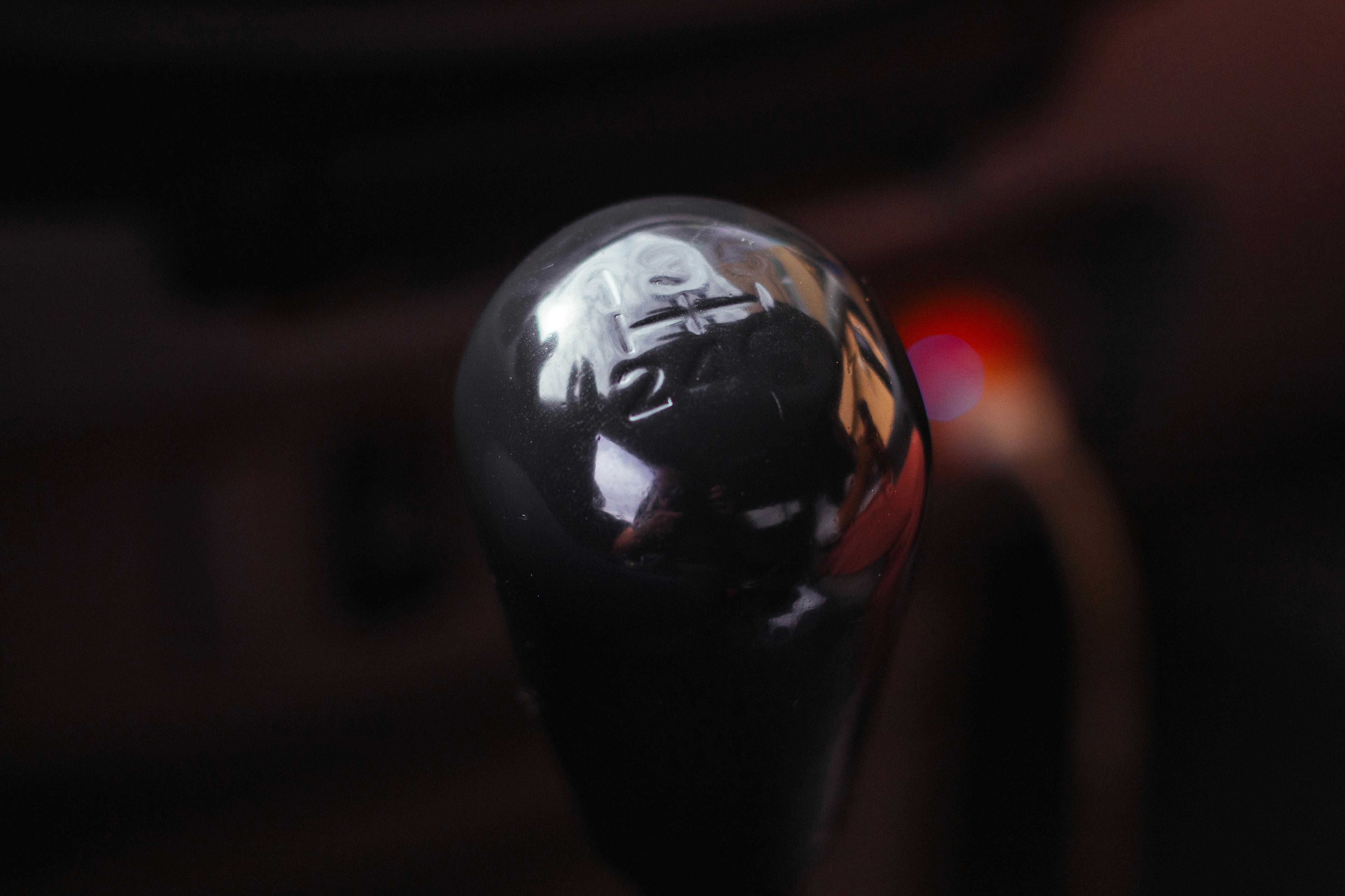 Close-up photograph of a reflective chrome gear knob inside a dim car interior, capturing the distorted reflection of the photographer.