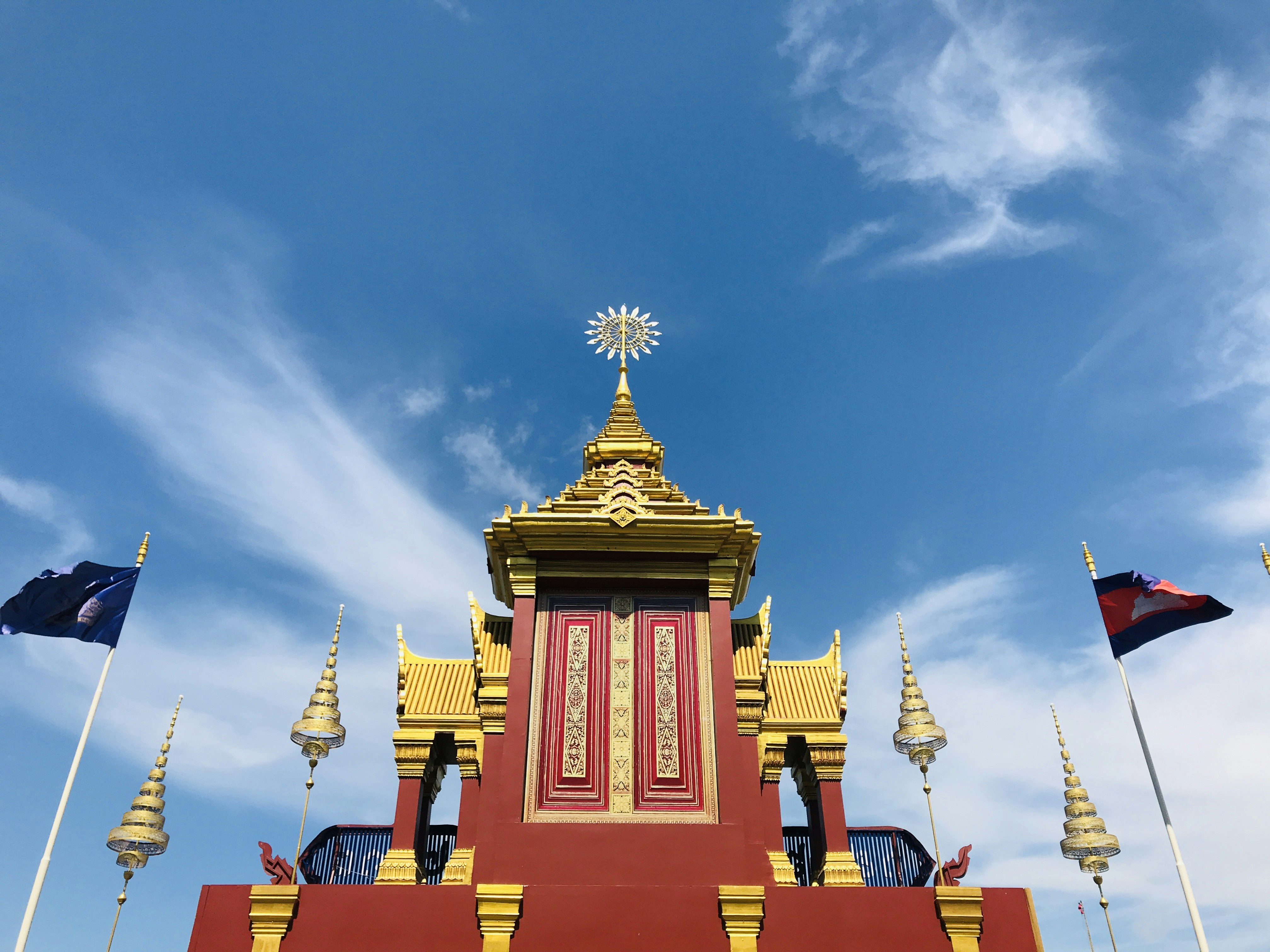 Ornate red and gold architectural structure with flags under a vibrant blue sky.