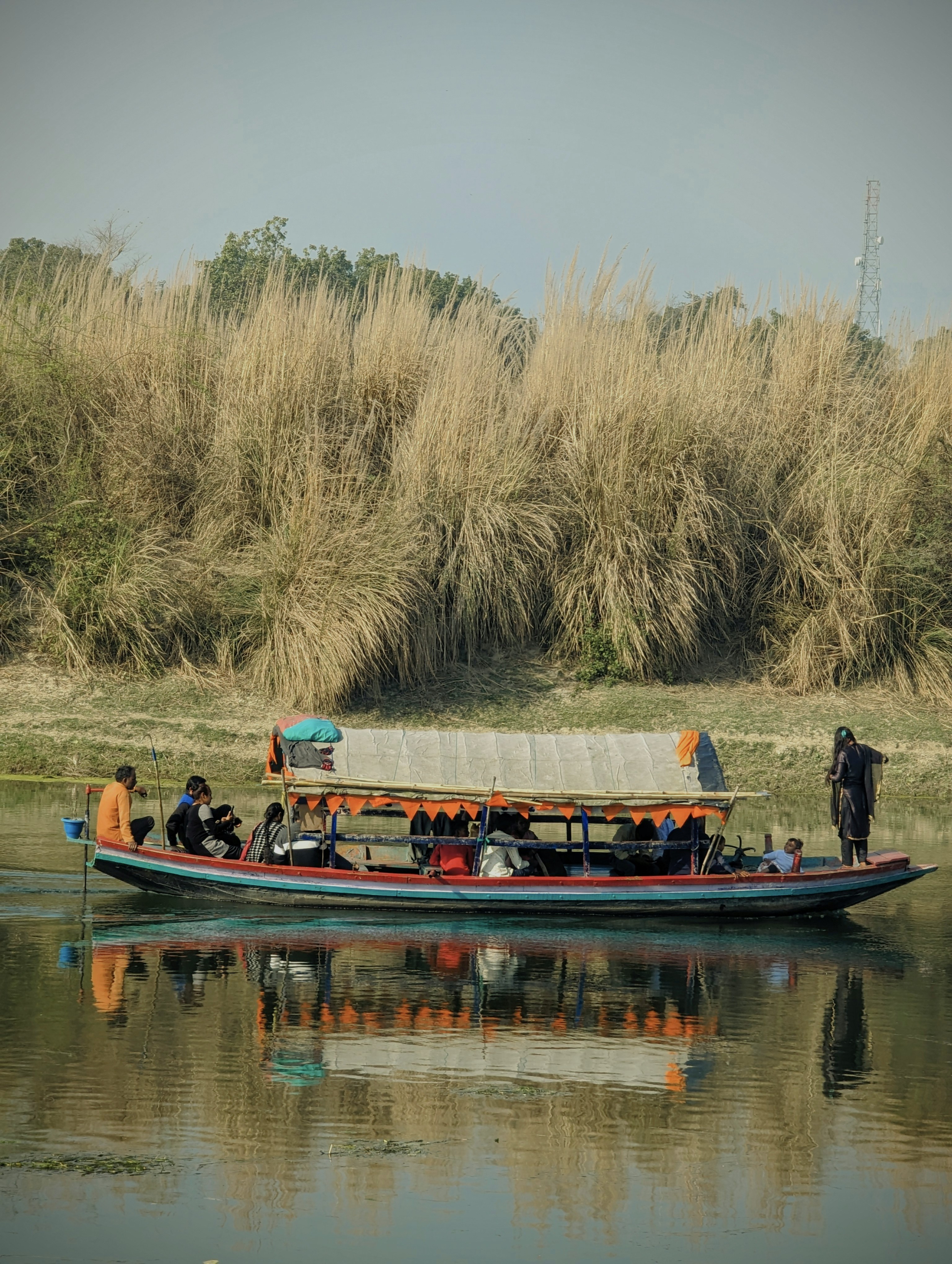 Sunlit River Crossing: Passengers Aboard a Colorful Boat Among Golden Reeds