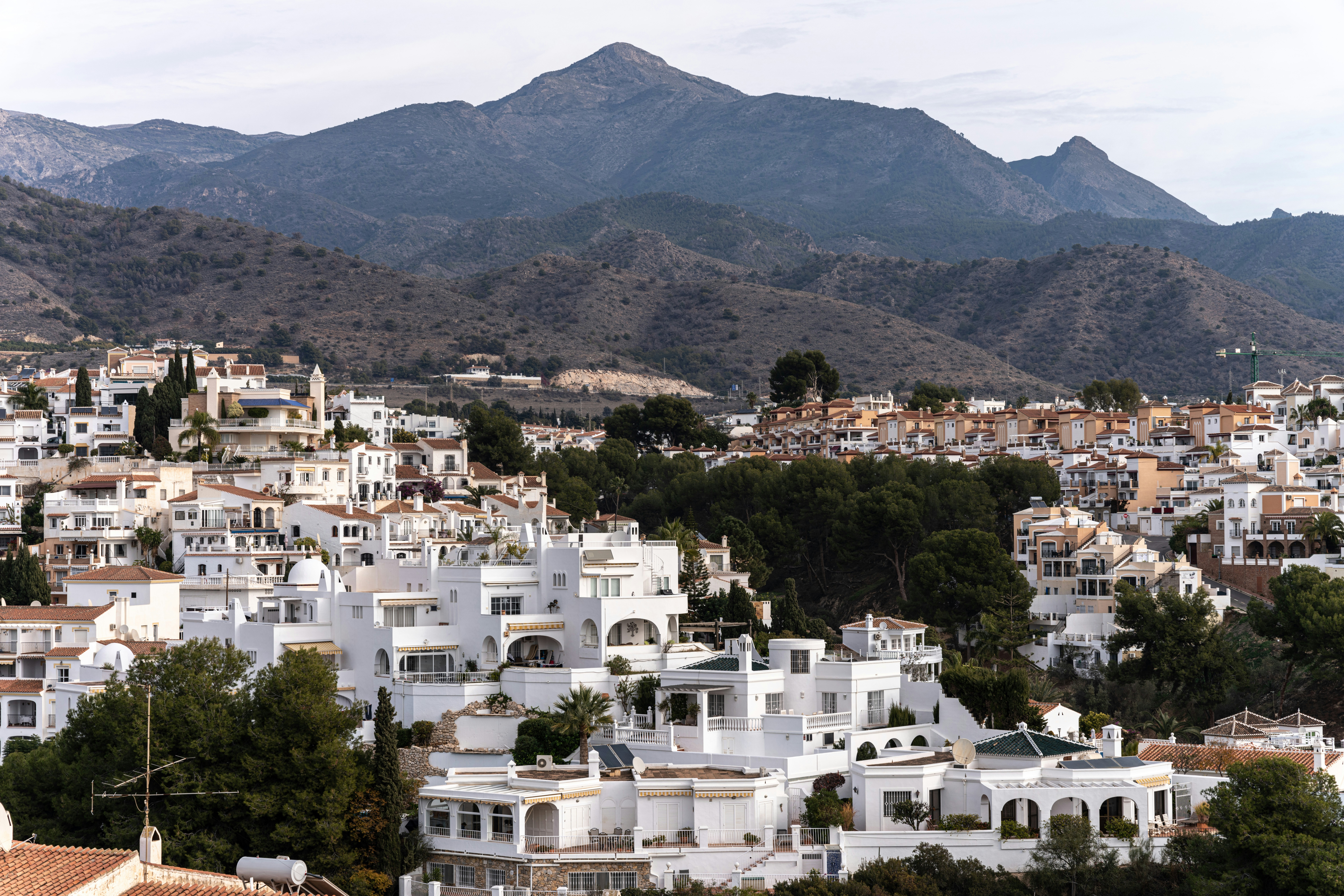 Whitewashed buildings nestled against a mountainous backdrop under a cloudy sky.