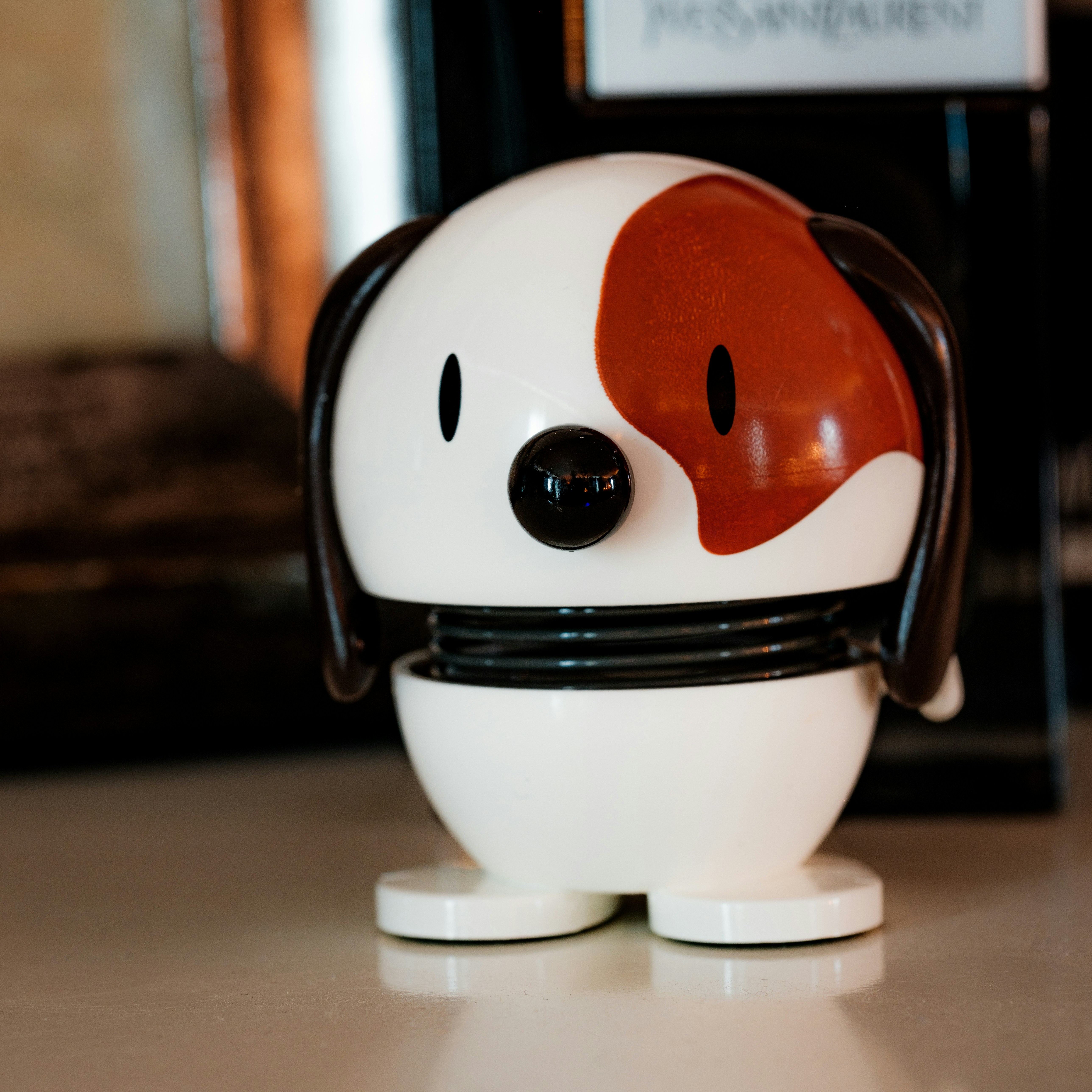 One-Patch Pup: A Glossy Ceramic Dog Figurine in Warm Indoor Light