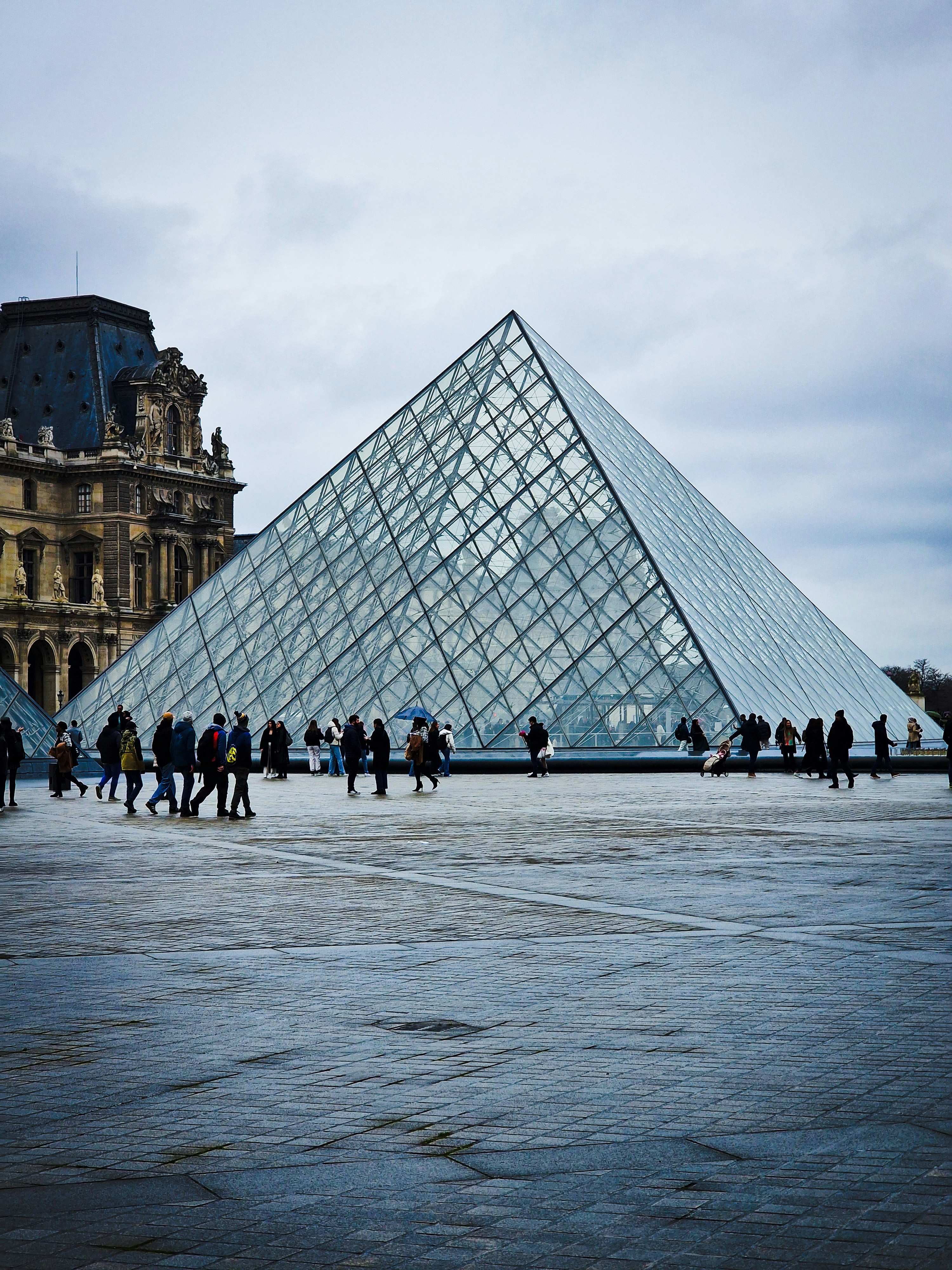 A group of people standing in front of a large glass pyramid photo ...