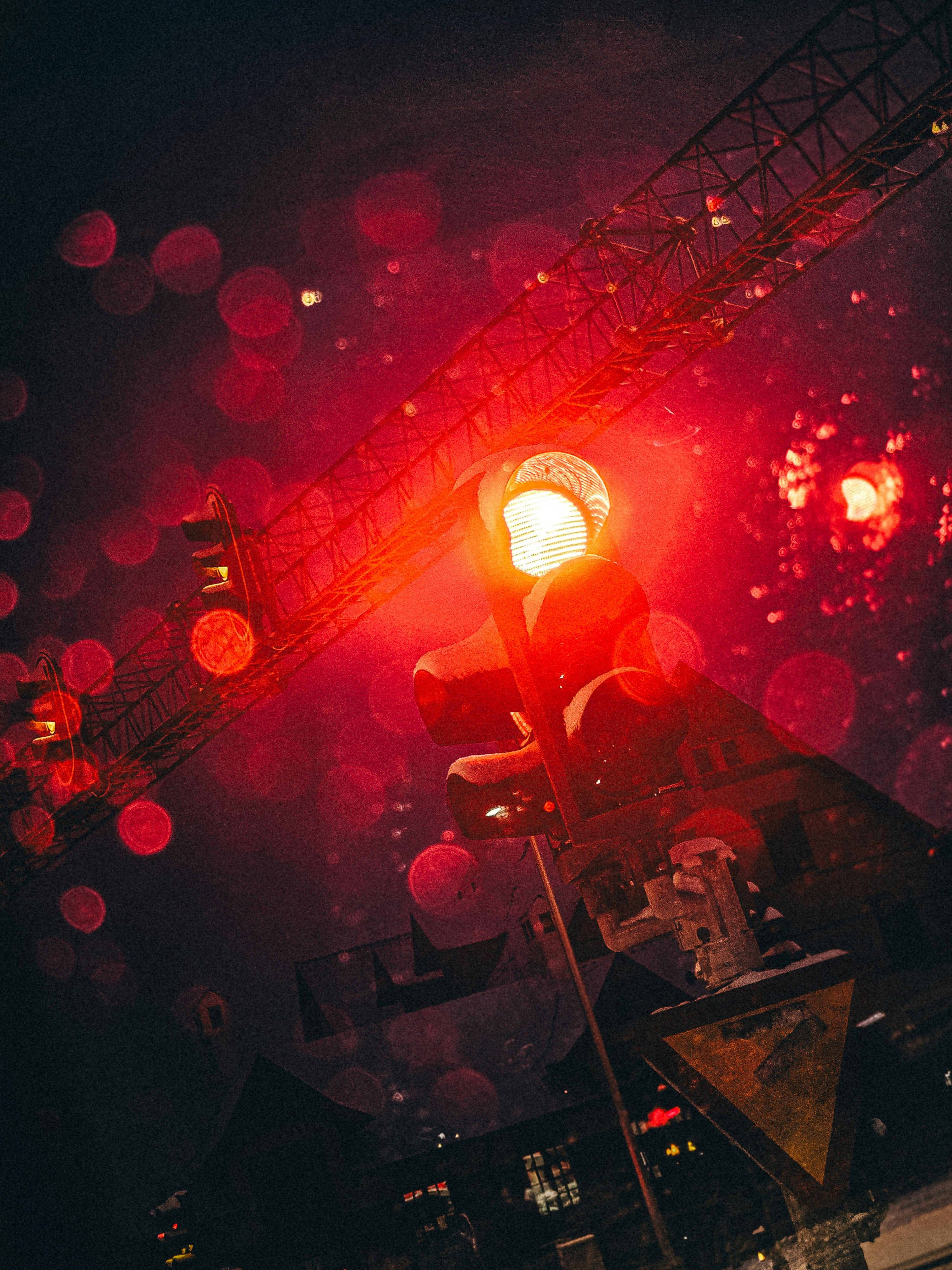 Night street photograph focusing on a glowing red traffic light, with a construction crane and red bokeh orbs in the background.