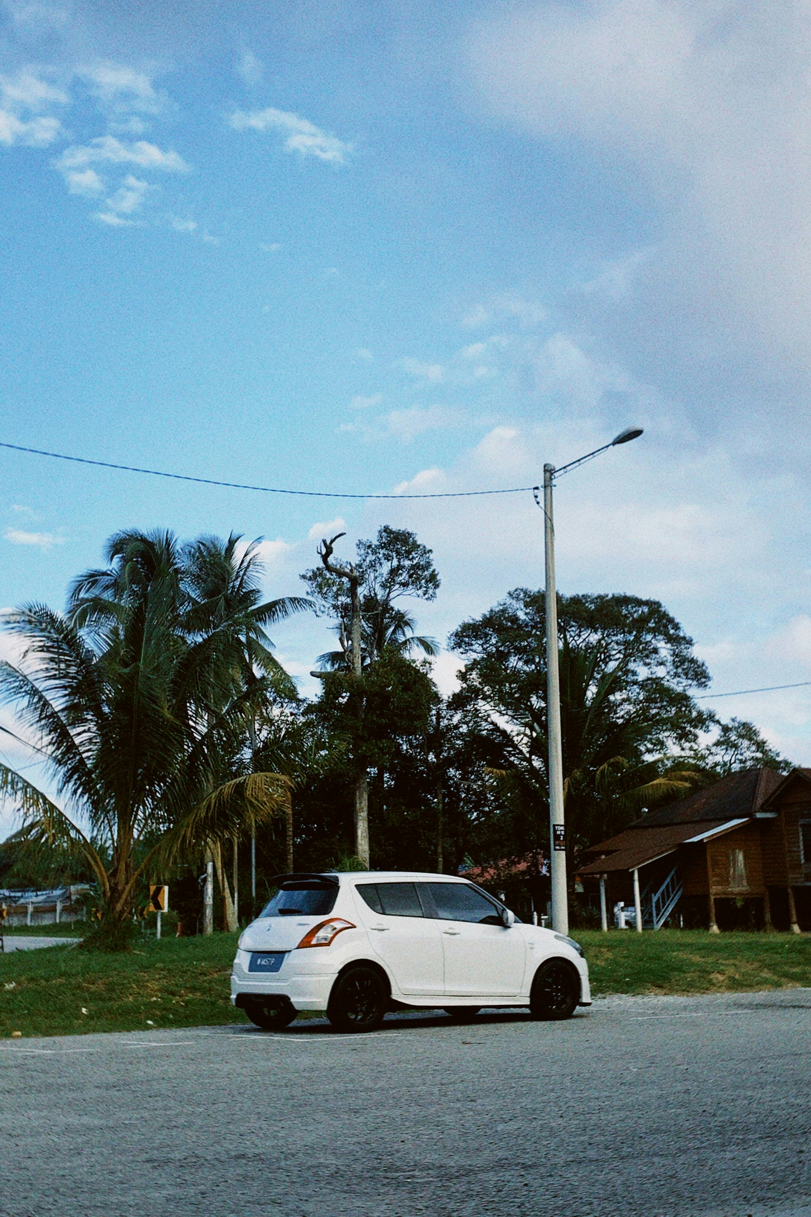 White compact car parked beside palm trees under a vast blue sky, capturing a moment of tranquility in an urban setting.