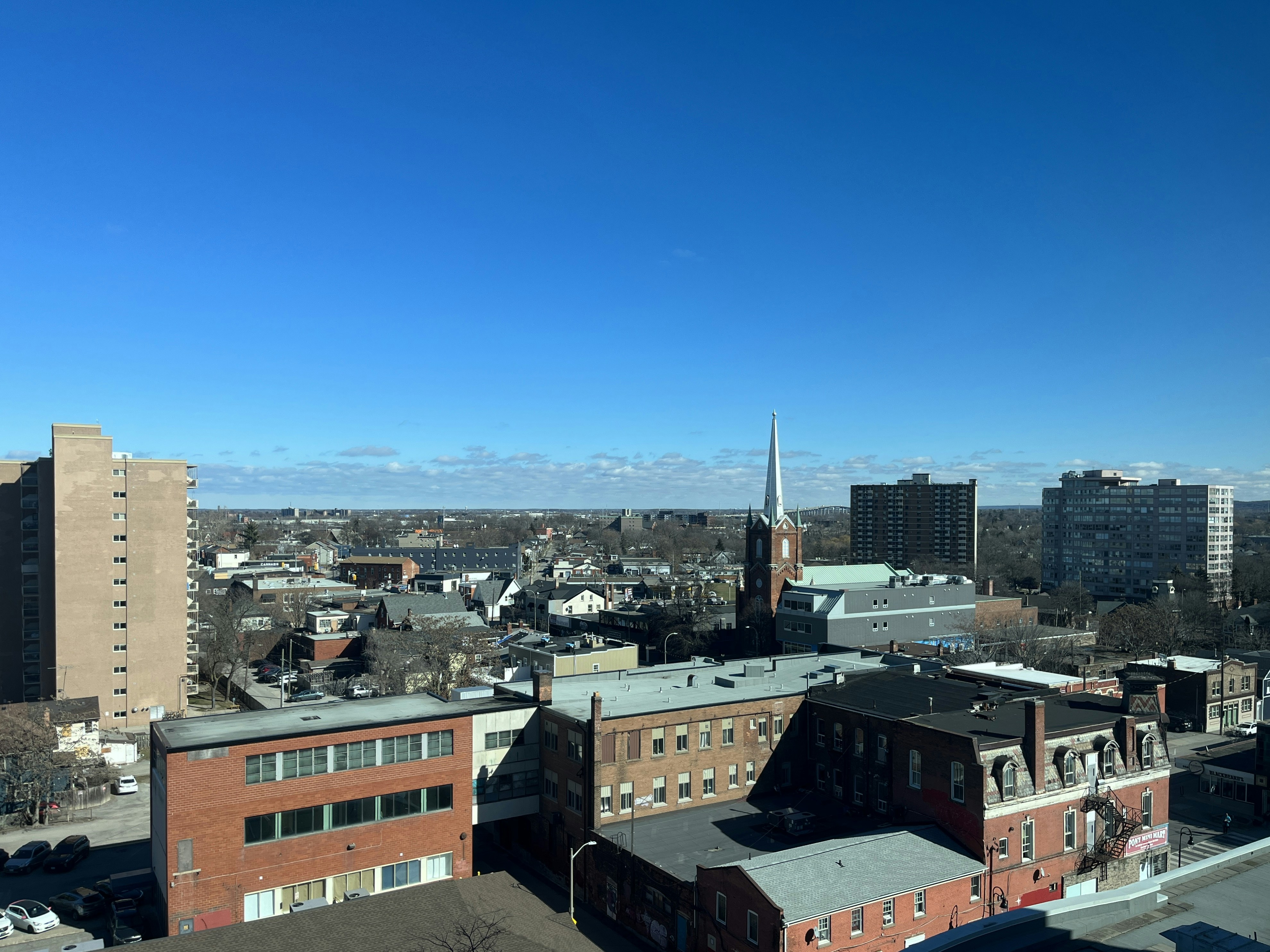 A panoramic view of a cityscape featuring a mix of modern and historic architecture under a clear blue sky. The prominent church steeple adds character to the urban landscape.