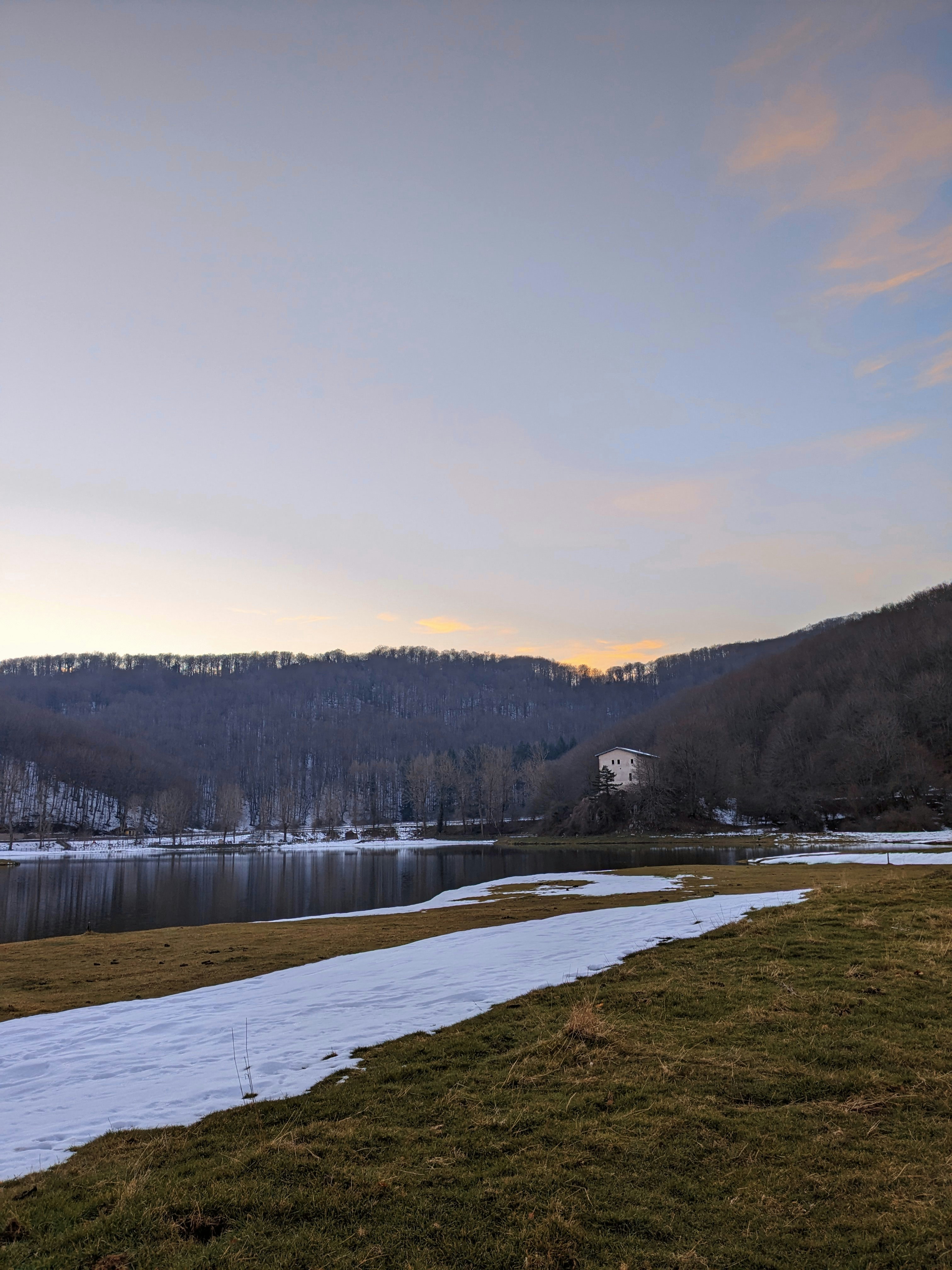 Dusk at Snow-kissed Shore: A Lone Hillside House Framing the Lake