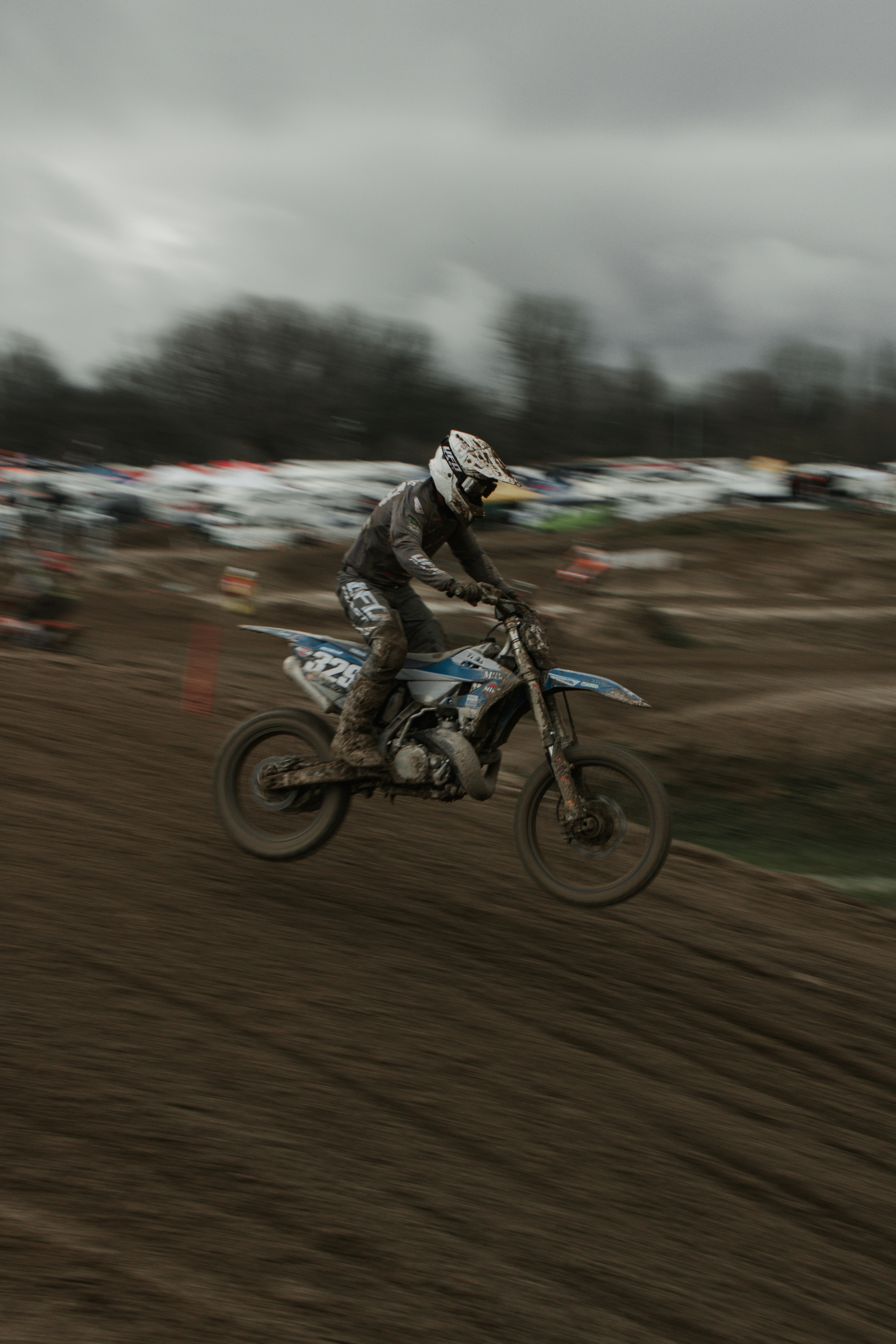 Blue Moto in Flight: Muddy Track, Overcast Sky, and a Moment of Lift